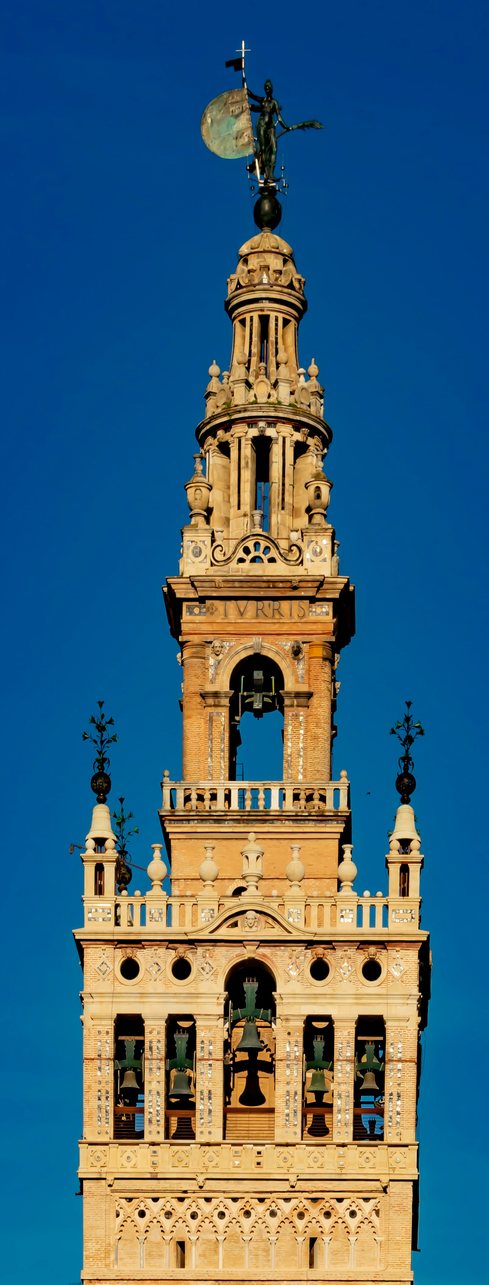 Intricately designed bell tower adorned with a statue, showcasing architectural elegance against a clear blue sky.