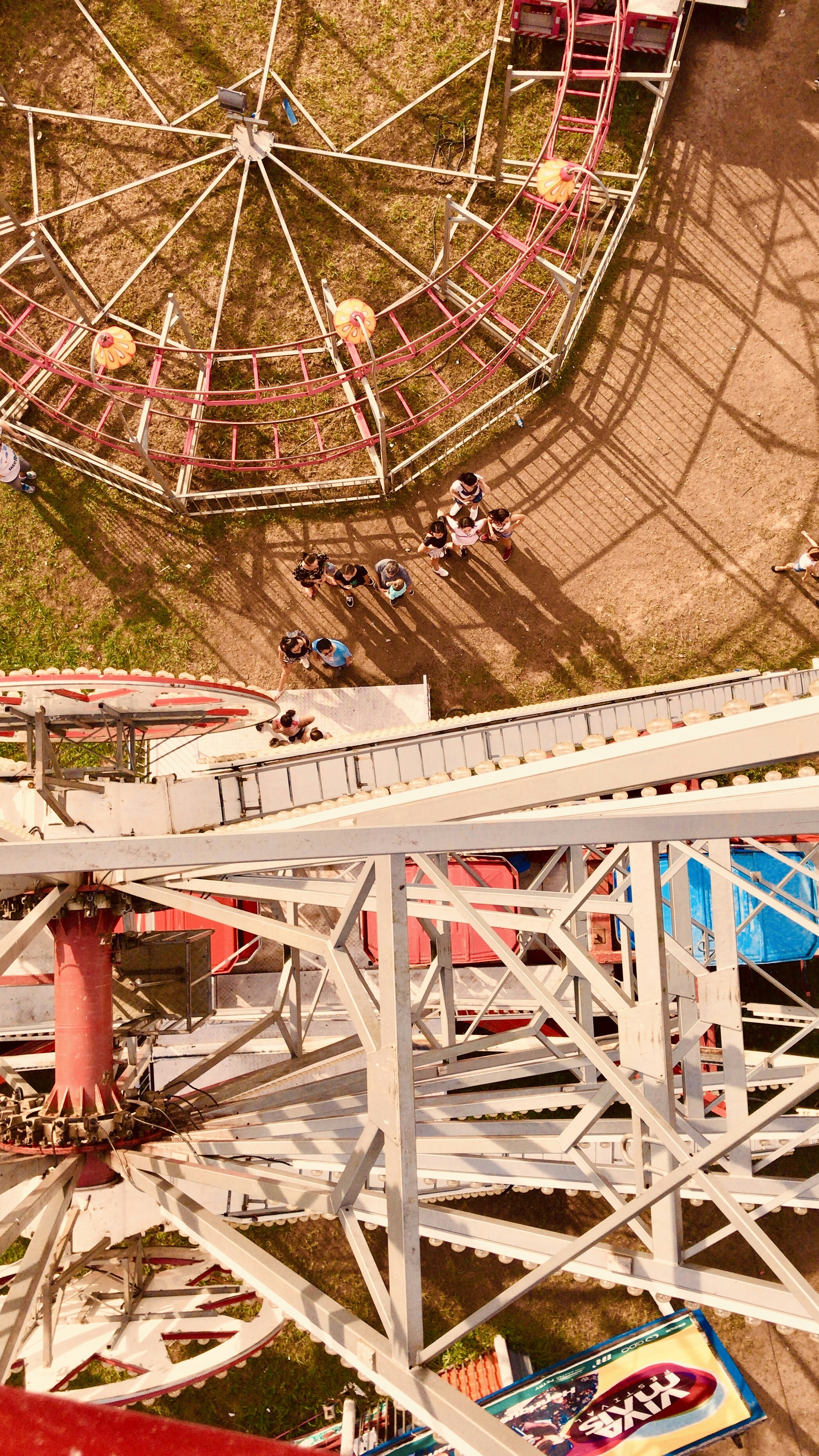 Photo from the Ferris wheel top looking down. Some people wait on the line at the neighborhood carnival park, during the day.