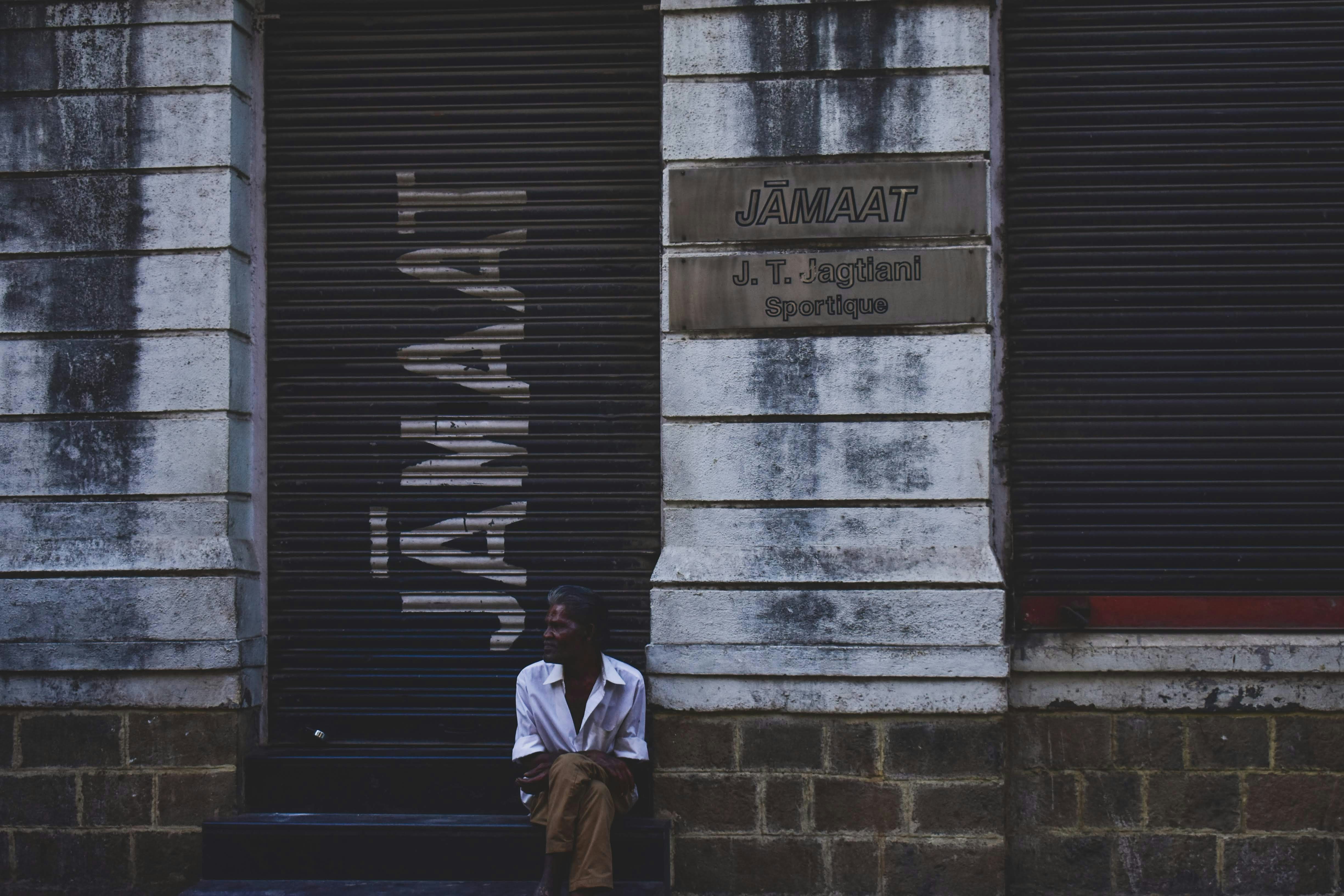 Shadowed doorstep under Jamaat signage: a solitary figure on a shuttered streetfront