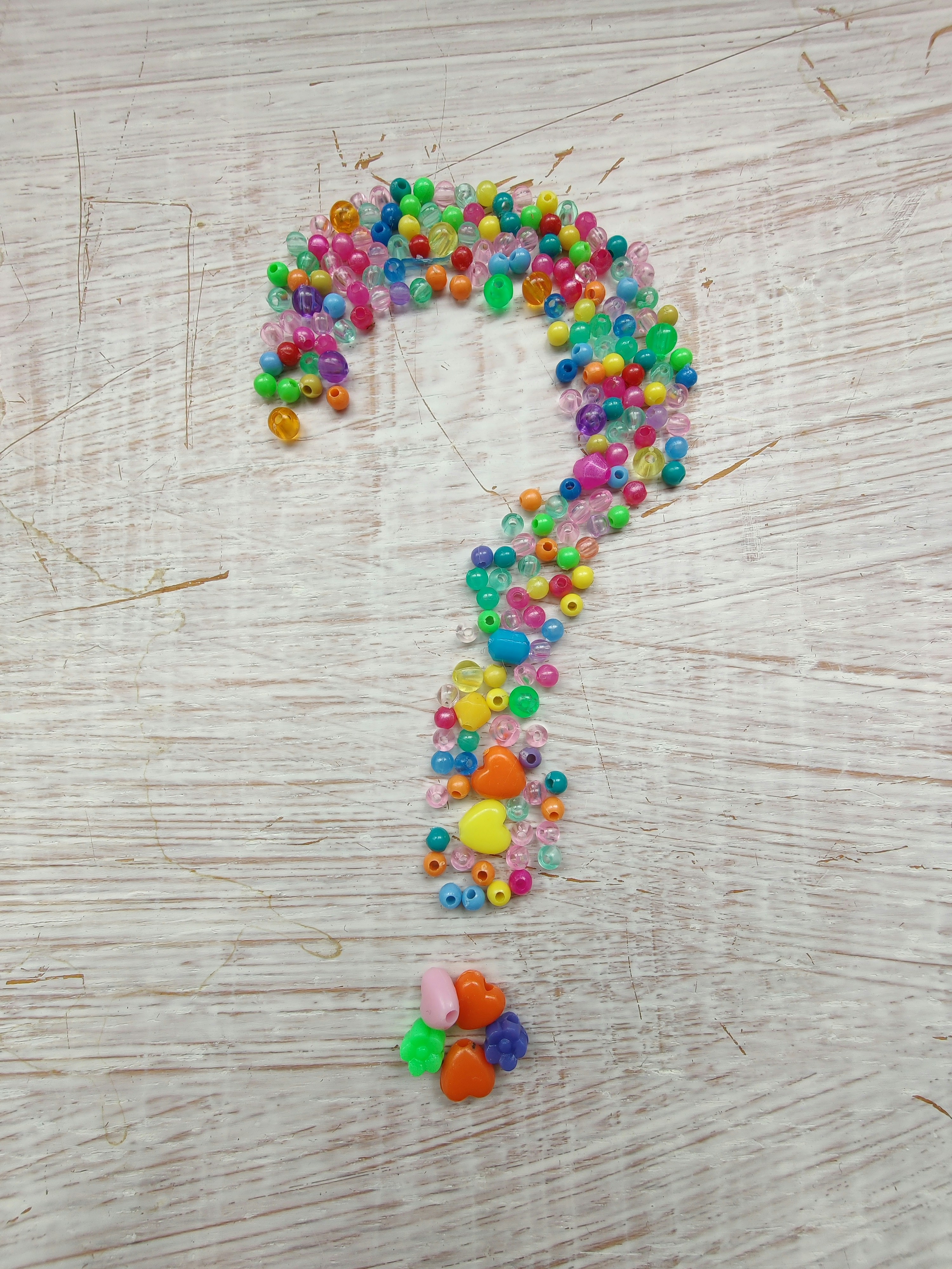Question Mark Made of Colorful Beads on Light Wood