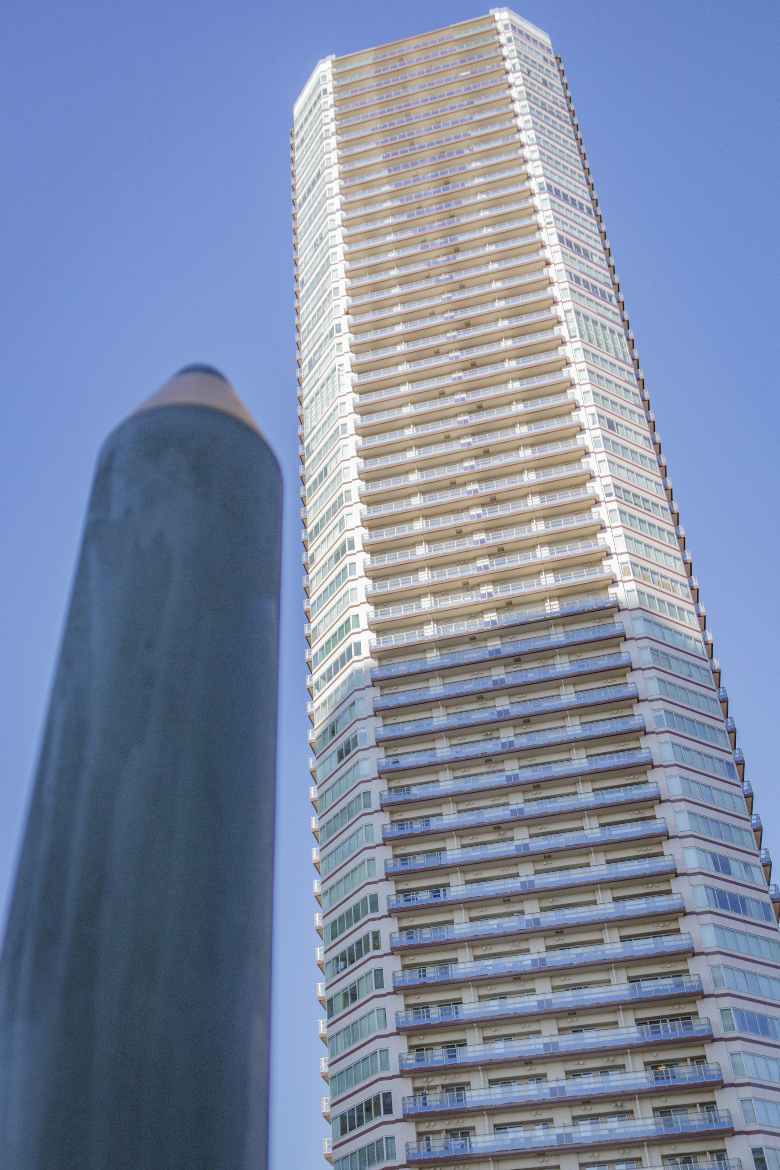 A towering skyscraper reaches for the sky, juxtaposed with a cylindrical structure in the foreground, illustrating modern architectural contrasts.