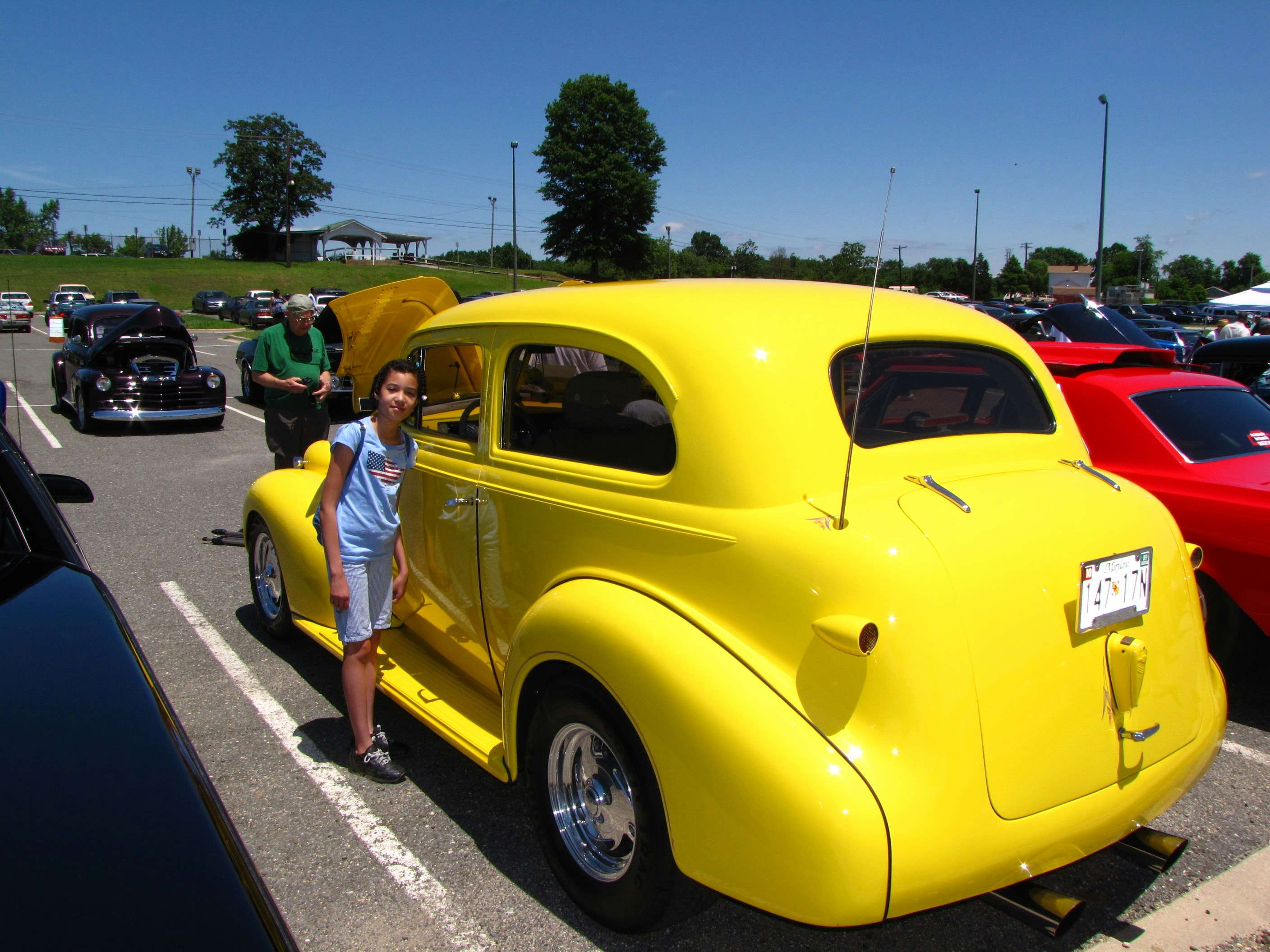 Yellow Classic: A child beside a vintage coupe at a sunlit car show