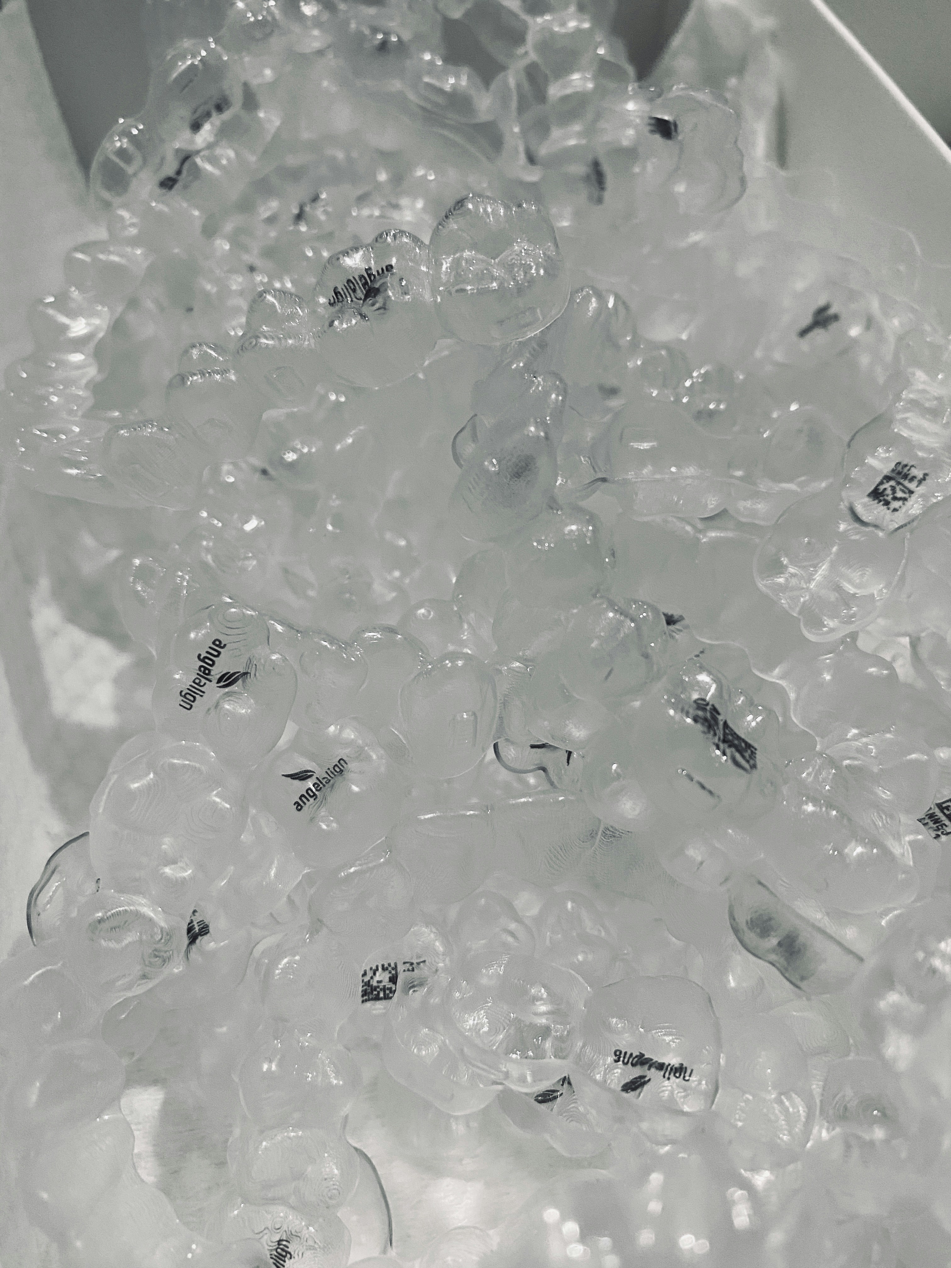 A close-up view of transparent objects intertwined, showcasing their intricate forms and subtle branding details. The composition highlights the interplay of light and transparency.