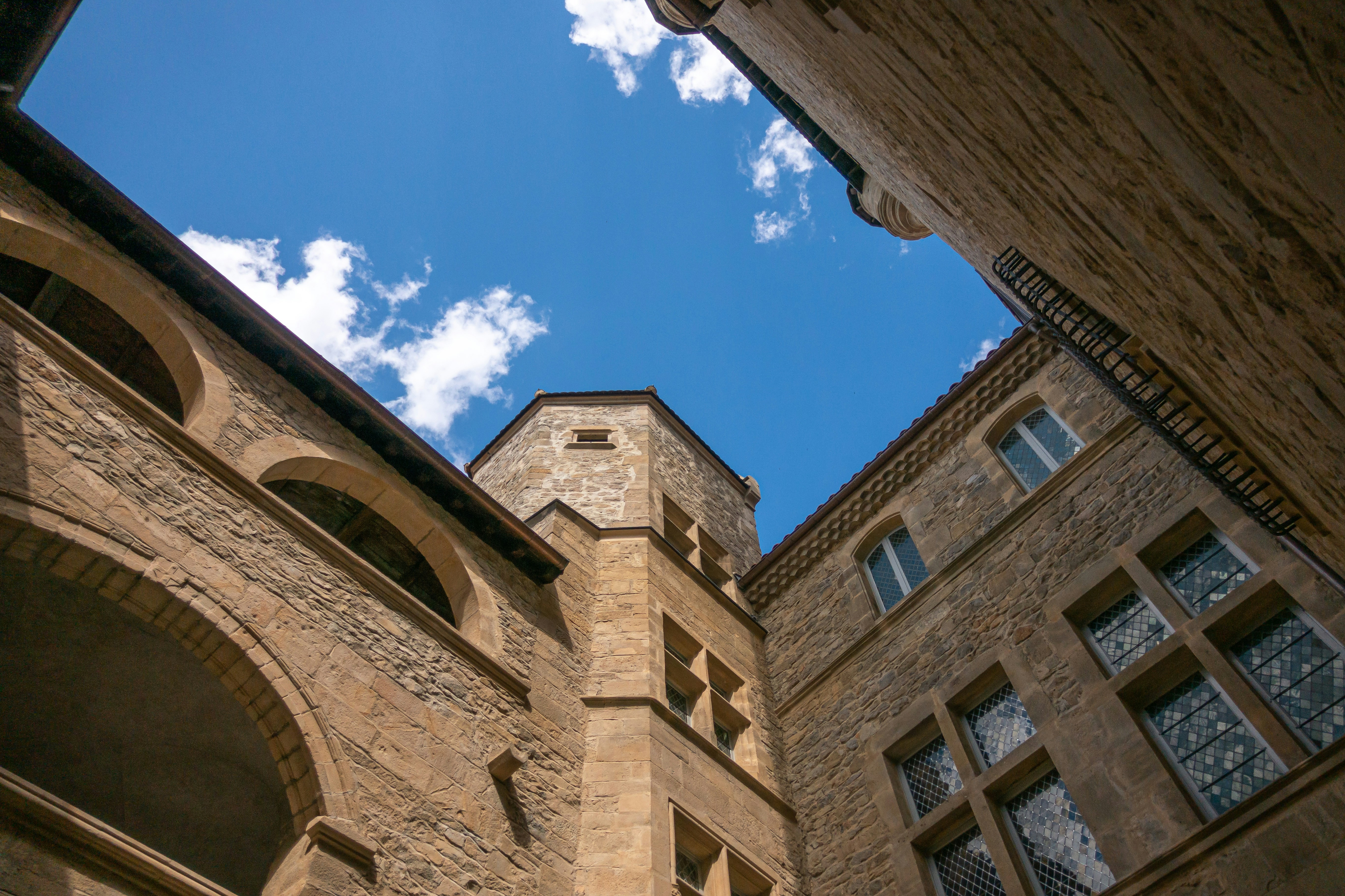 Looking up at a historic stone courtyard framed by elegant architecture and a vibrant blue sky.