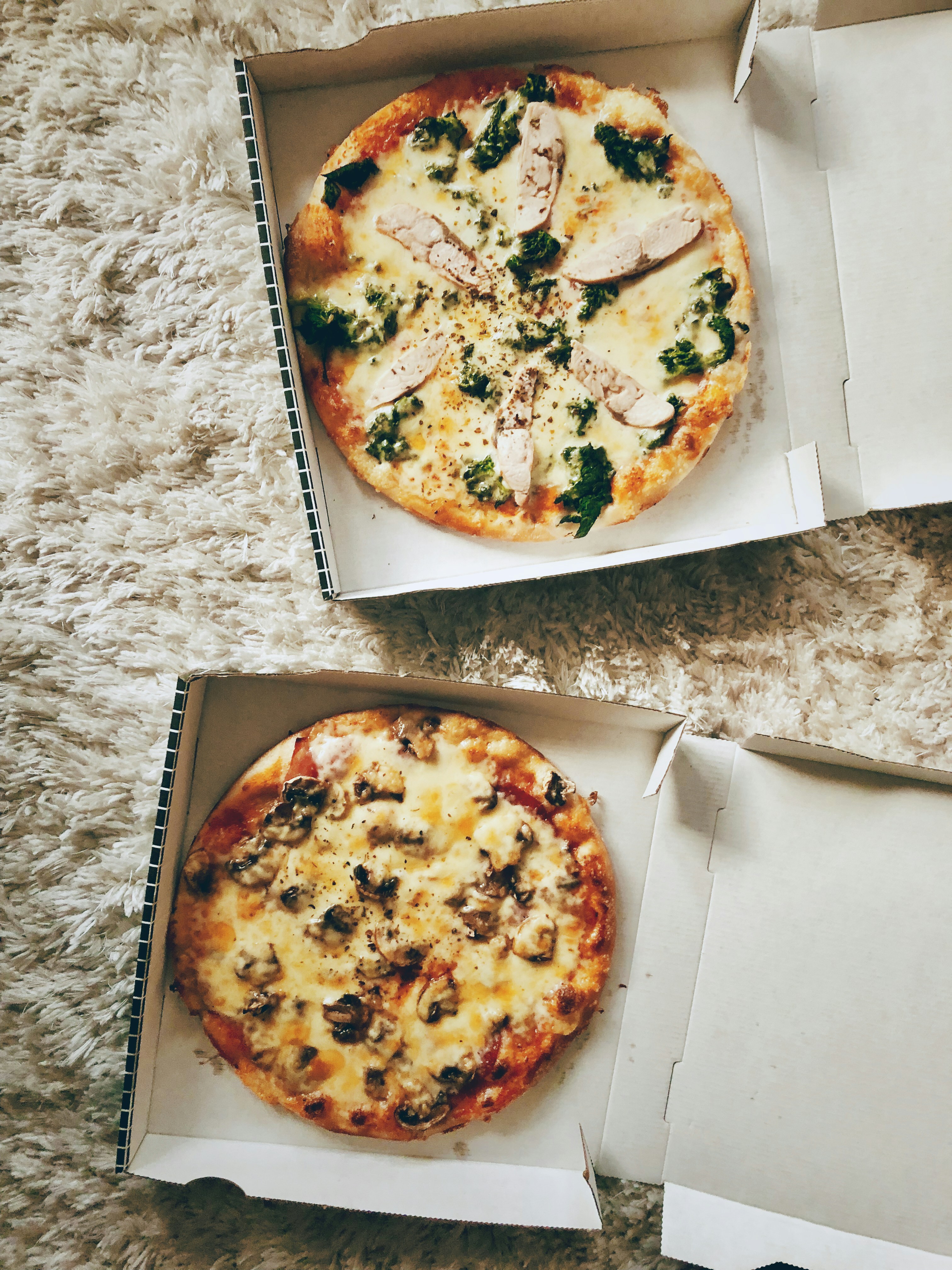 Two distinct pizzas presented in their boxes, one topped with chicken and broccoli, the other with a blend of cheeses and mushrooms.