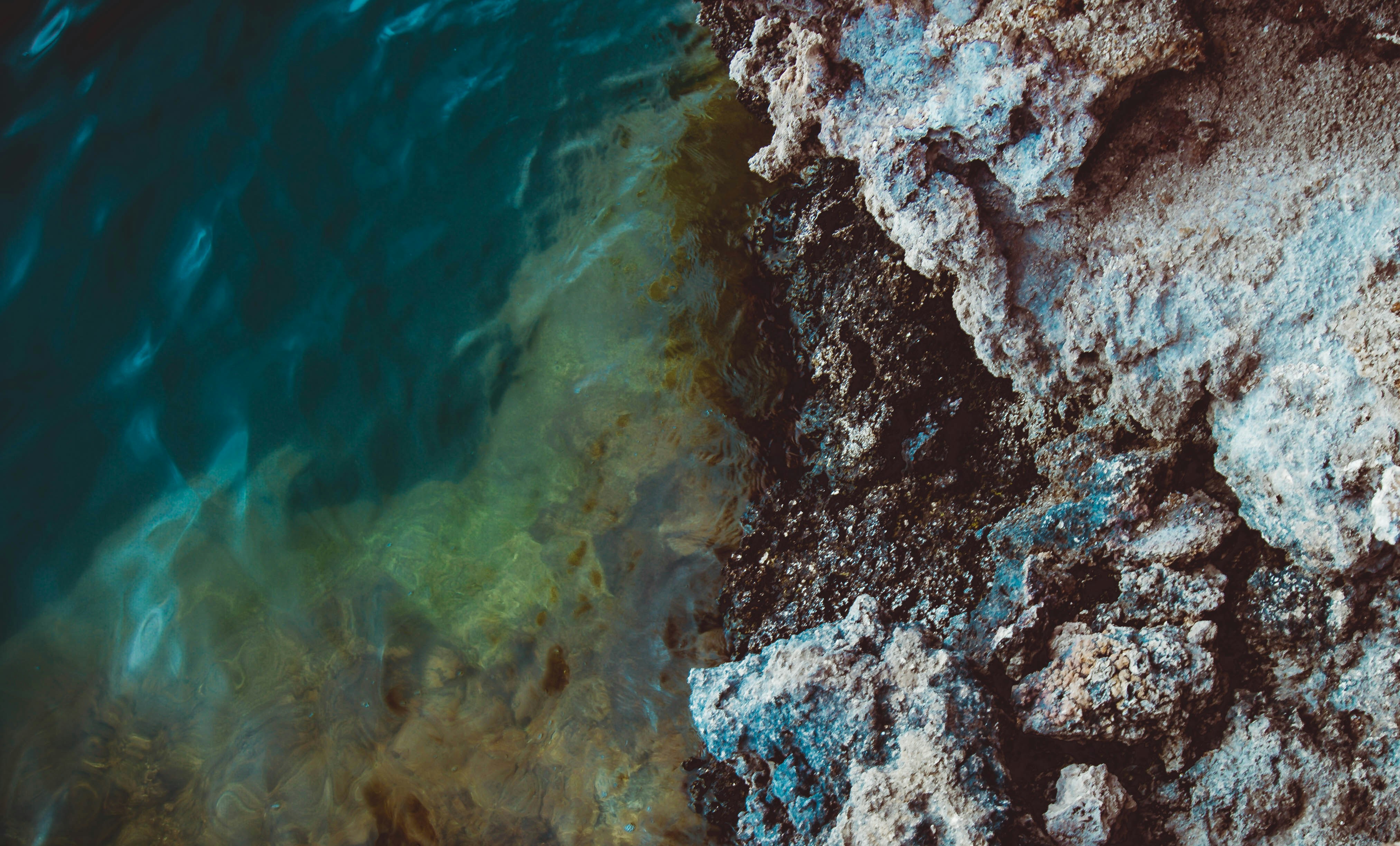 Rock formation with textured surfaces meets vibrant, turquoise water.