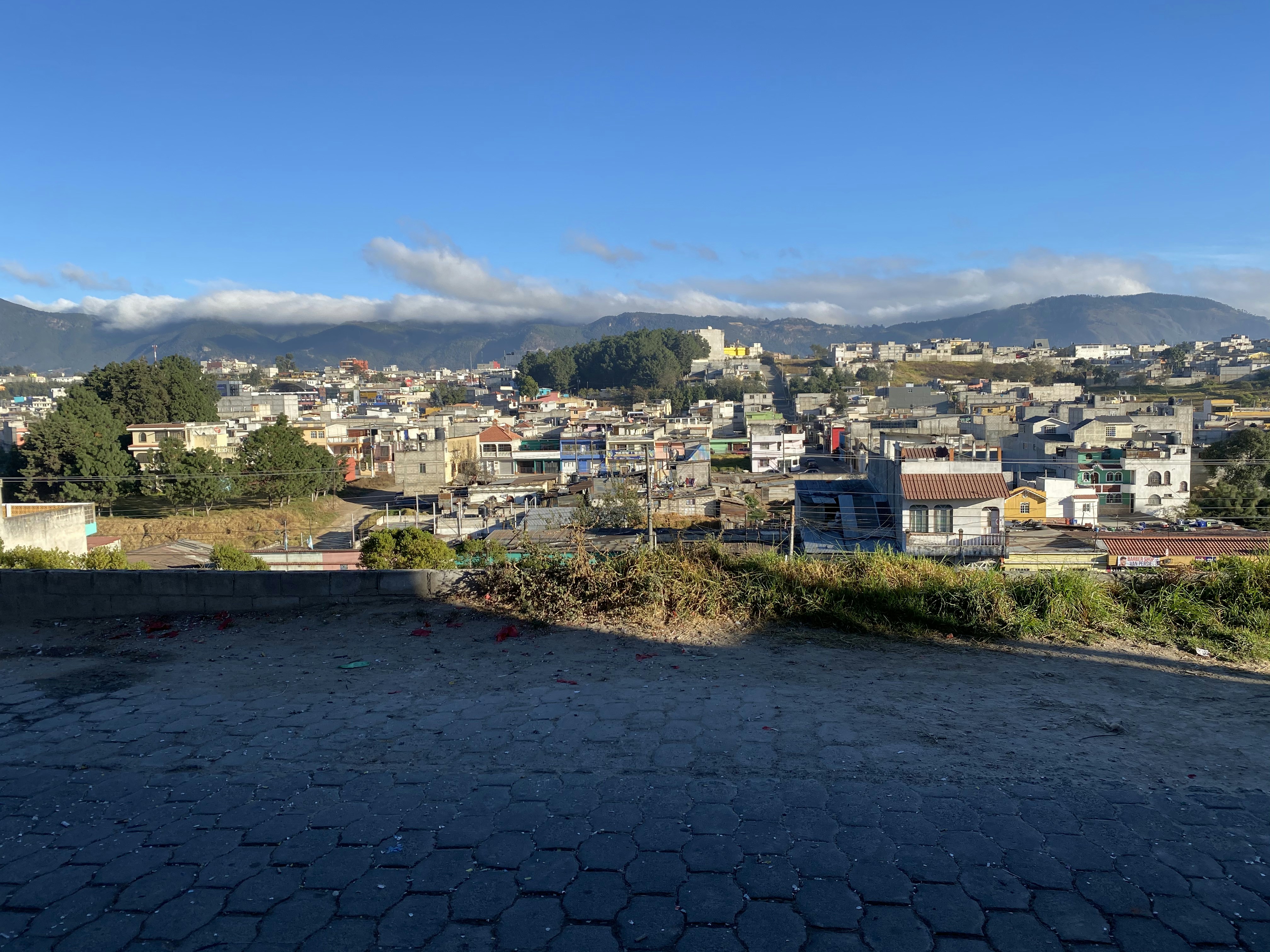 Panoramic view of a cityscape with diverse architecture set against distant mountains under a clear blue sky.