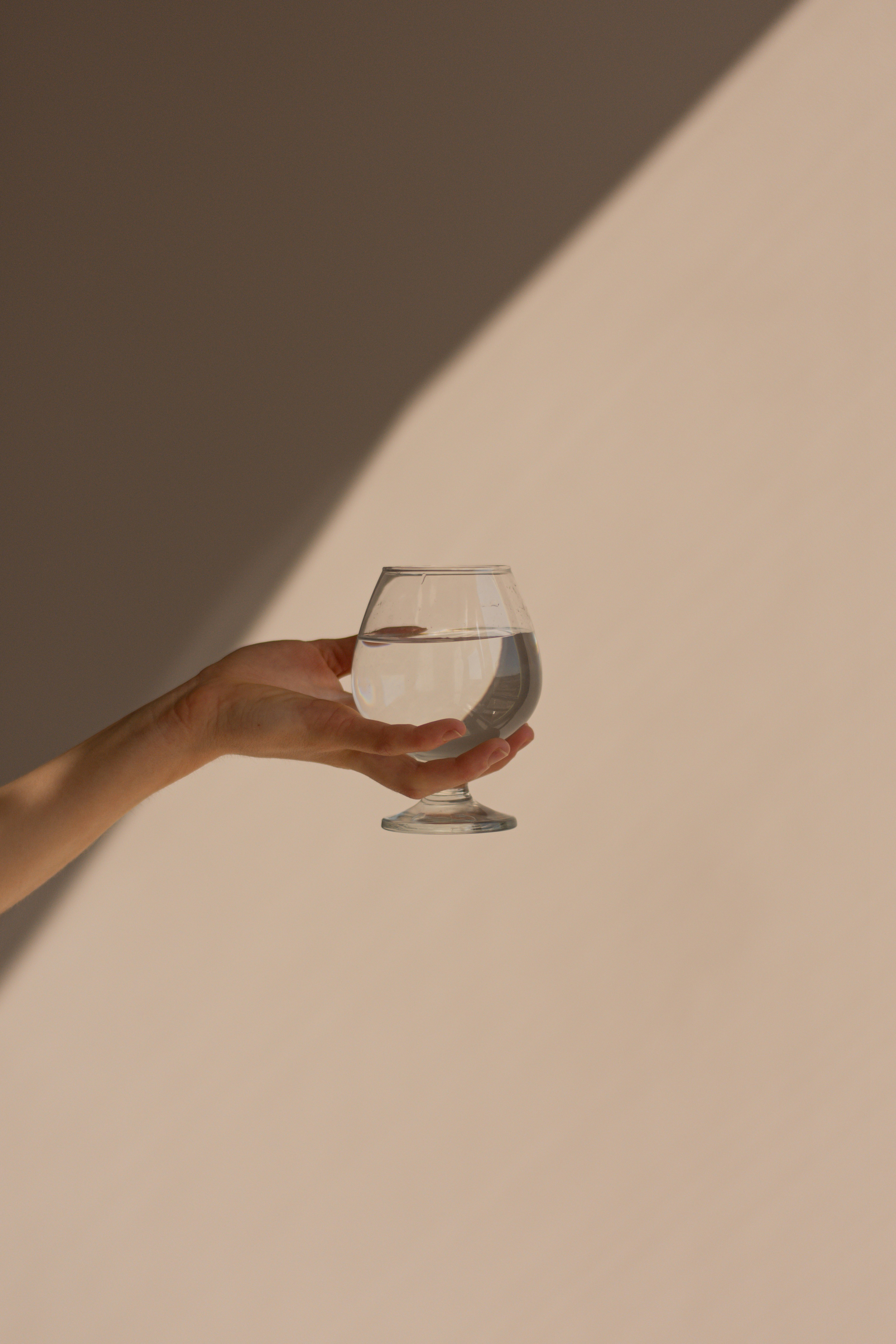 A hand elegantly holds a glass of water, casting soft shadows against a textured backdrop. The scene captures the interplay of light and transparency.