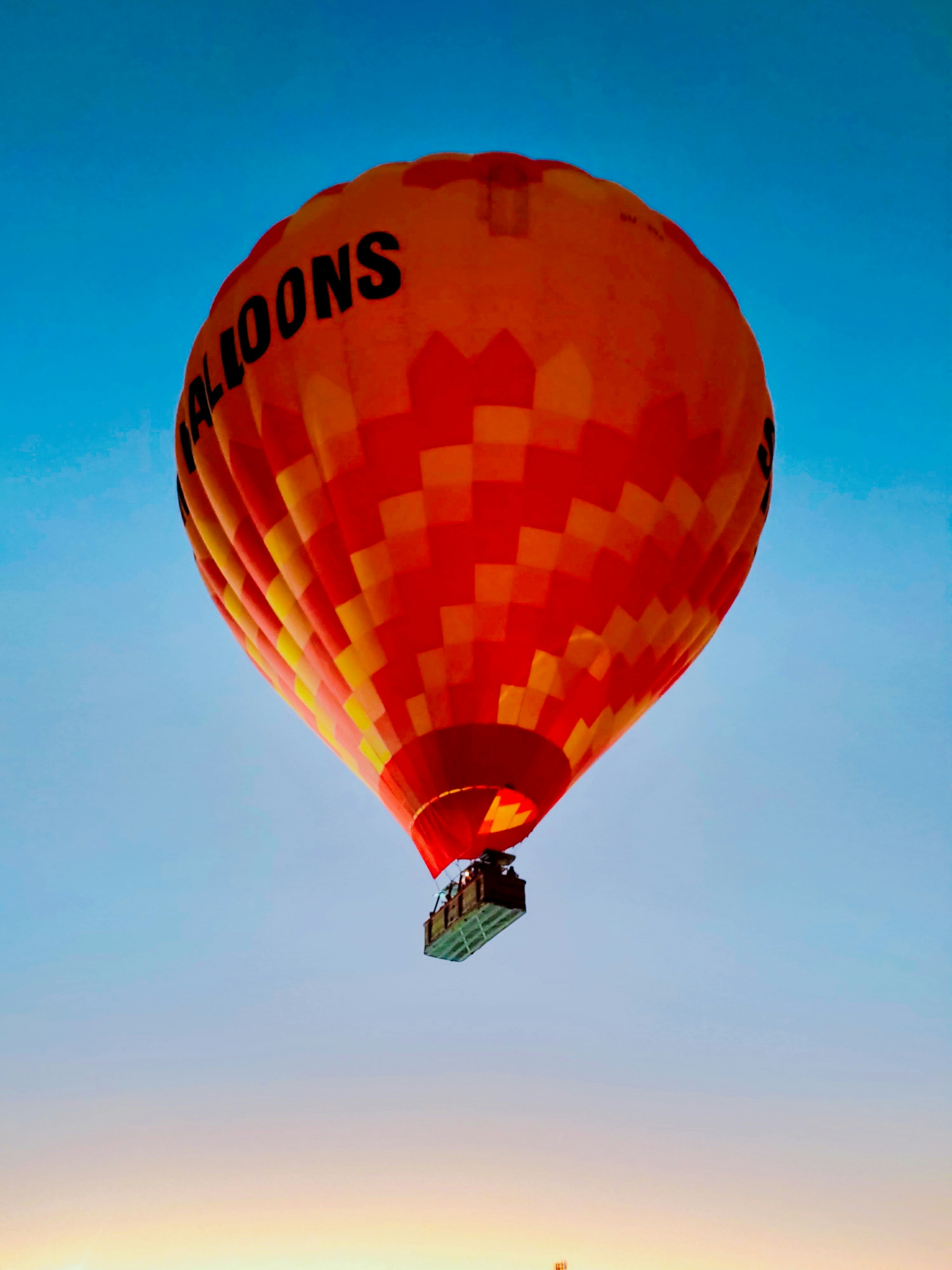 Red and yellow hot air balloon ascending against a clear blue sky at dusk.
