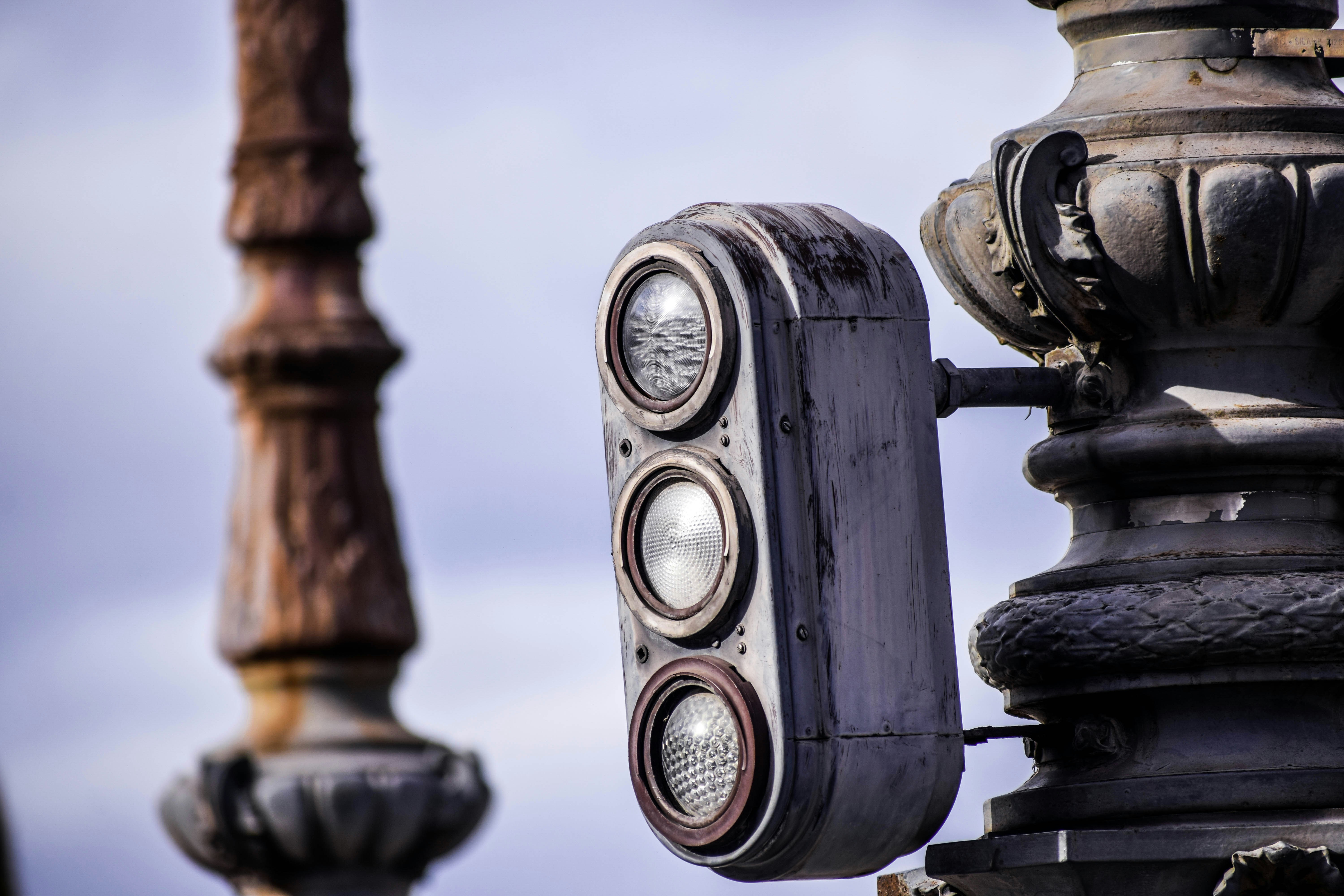 Three-Lensed Sentinel: Weathered Traffic Signal Clinging to an Ornate Street Lamp