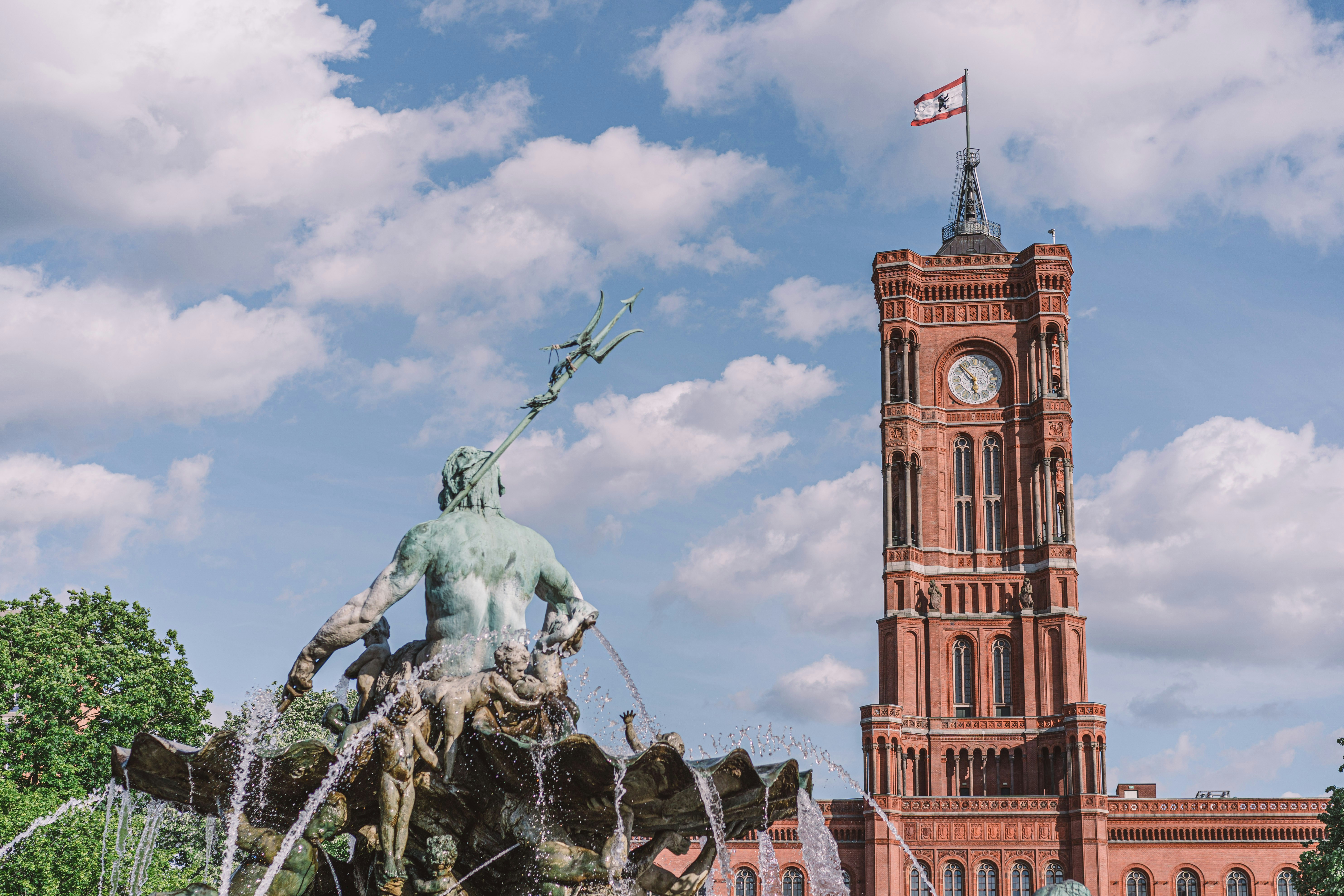 Neptune in Patina: Water Sprays Before Berlin's Red Rathaus Clock Tower