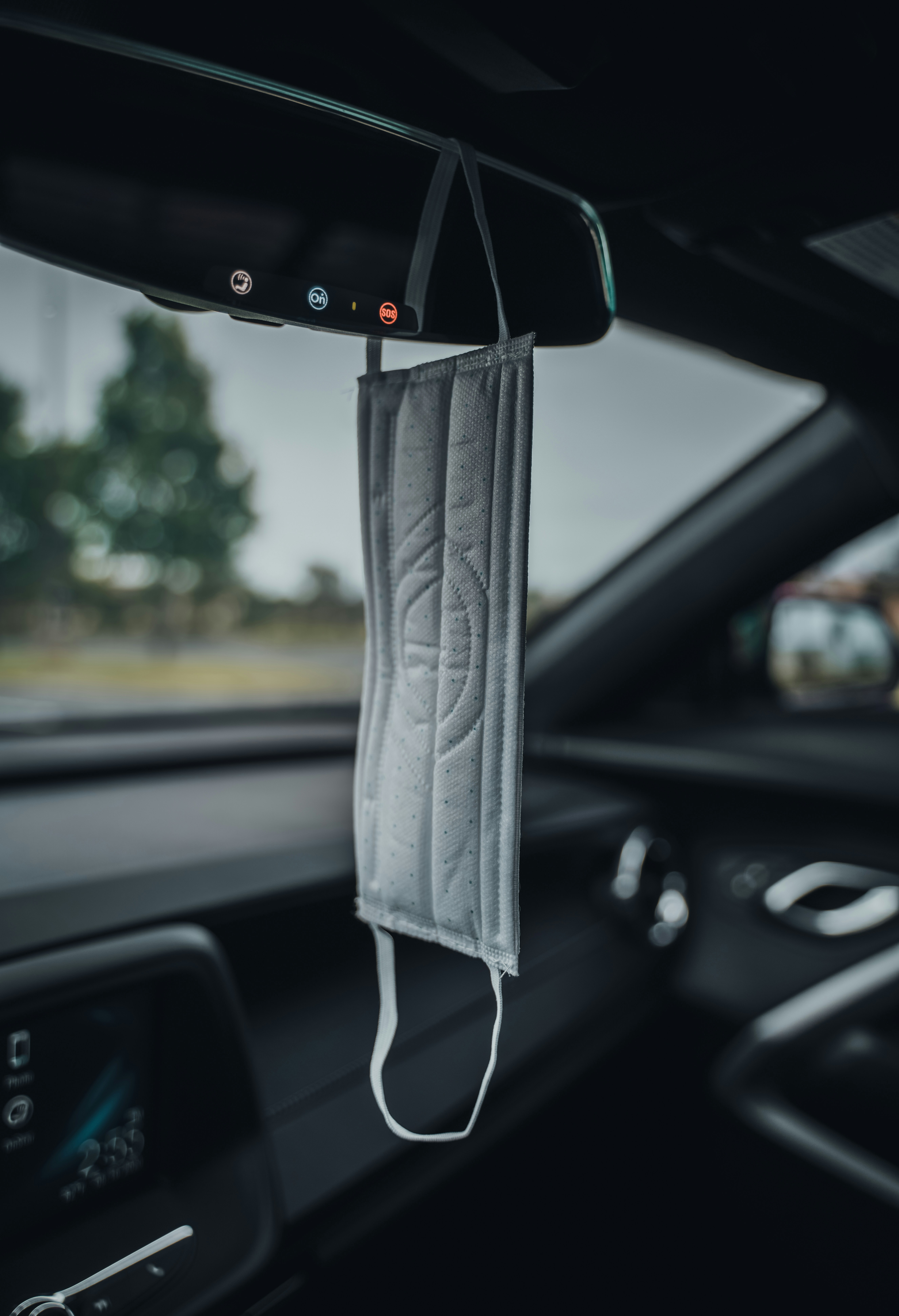 A white face mask hangs from the rearview mirror of a car, reflecting a moment of awareness and safety amid travel.