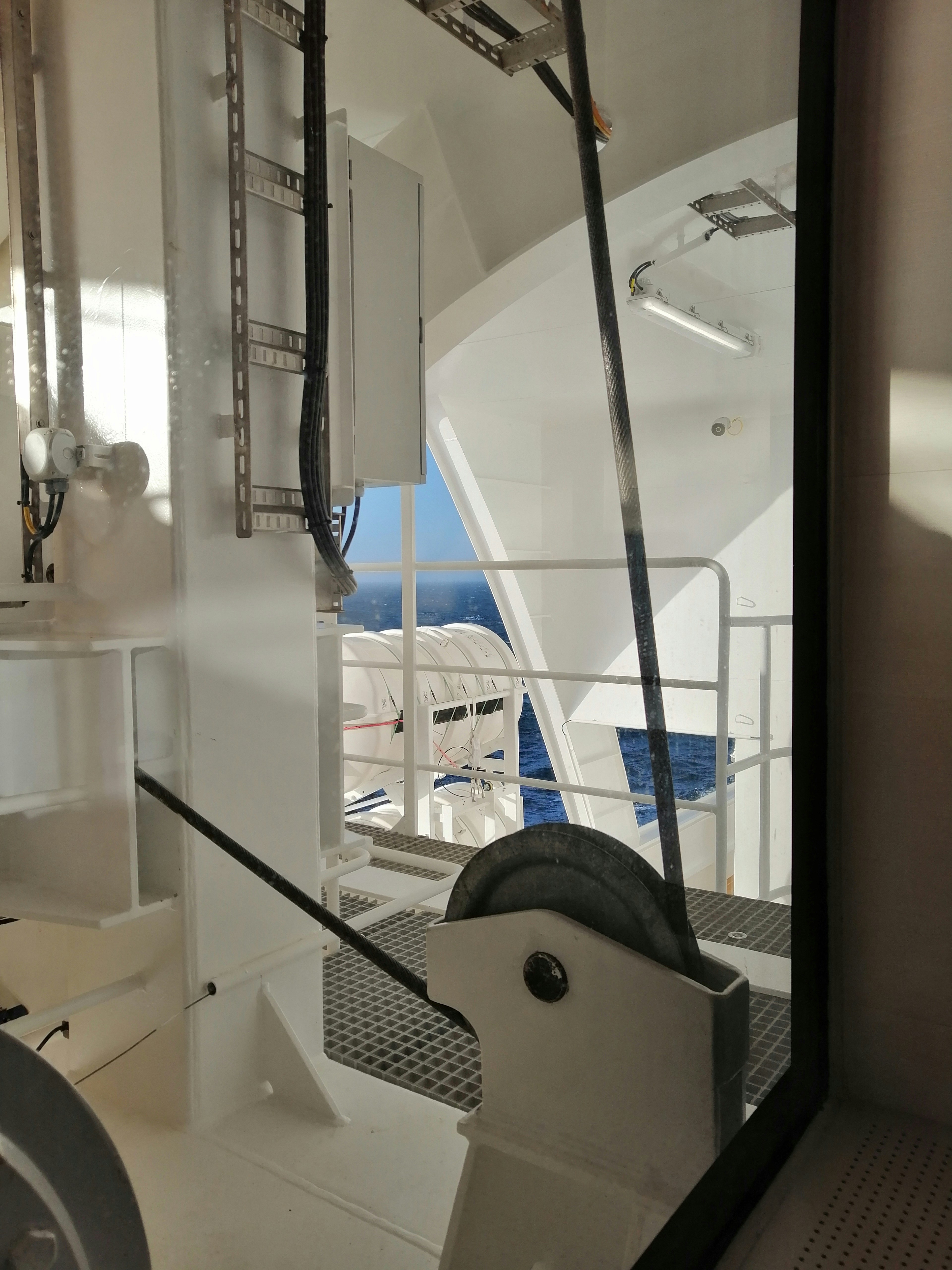 Interior view of a ship's machinery, showcasing a winch and control panel with ocean visible through the window.