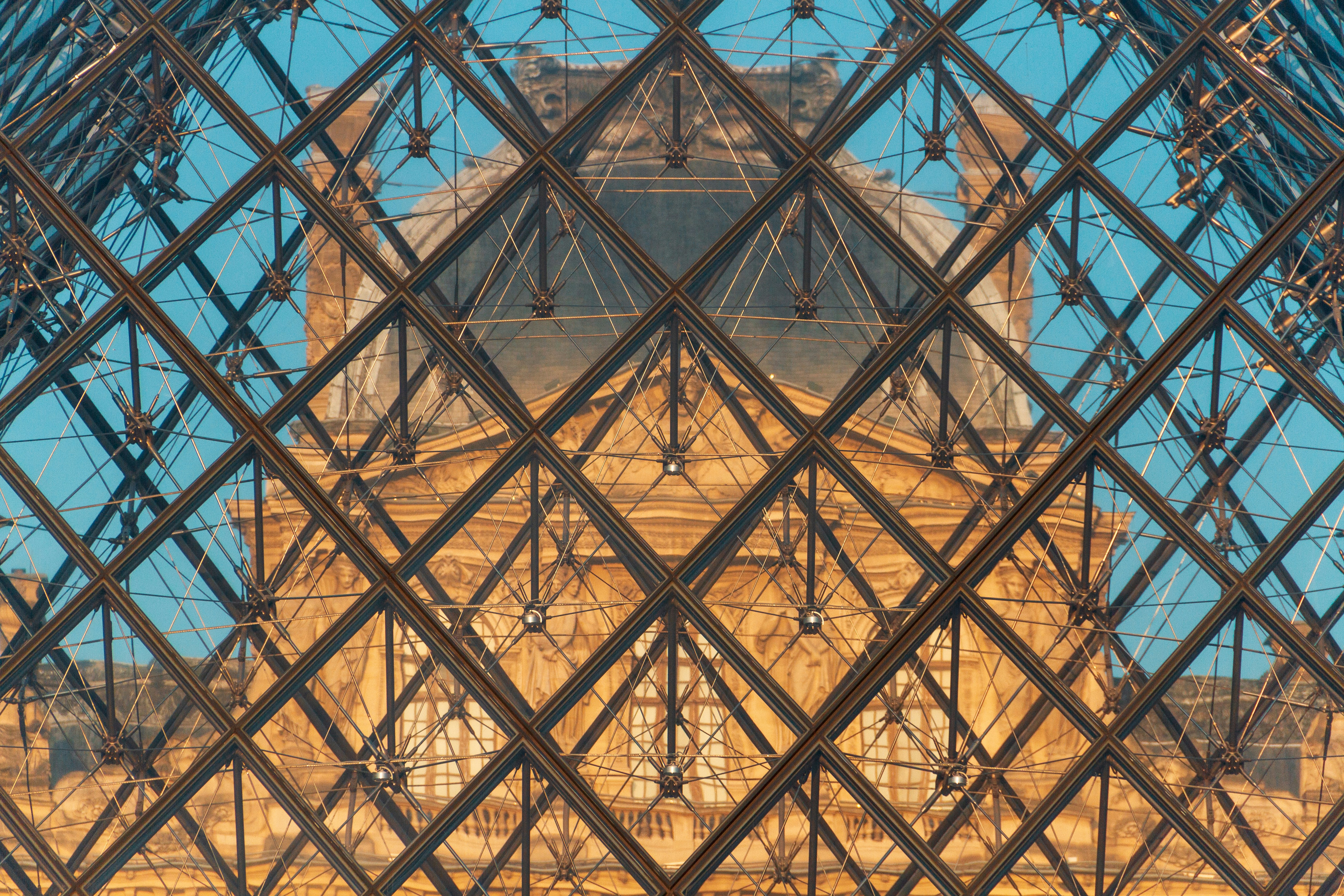 Intricate glass patterns of the Louvre's pyramid reflecting the historic architecture behind it.