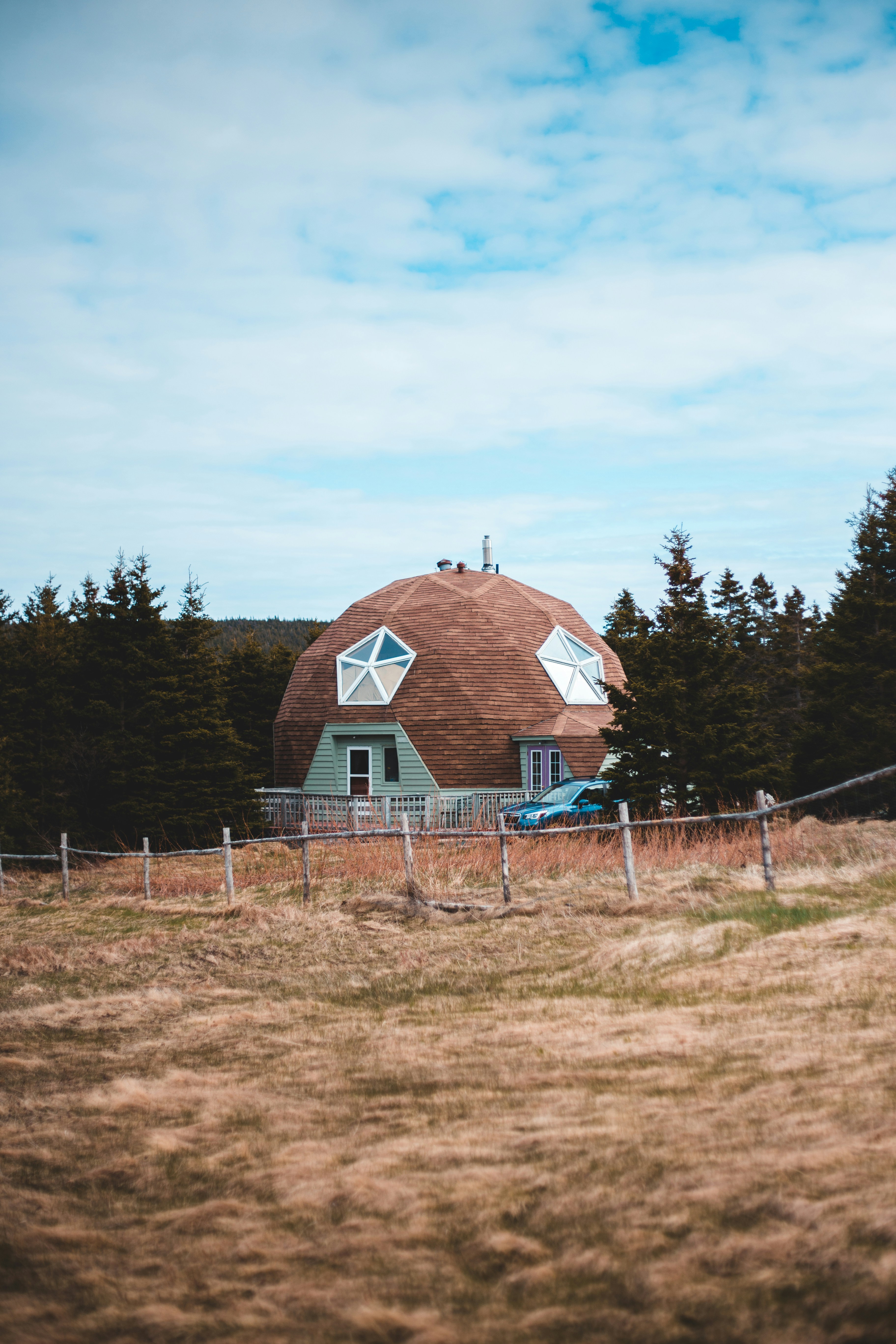 A geodesic dome house nestled among tall trees, showcasing a blend of modern architecture and natural surroundings. The structure features large windows and a distinctive roof design.