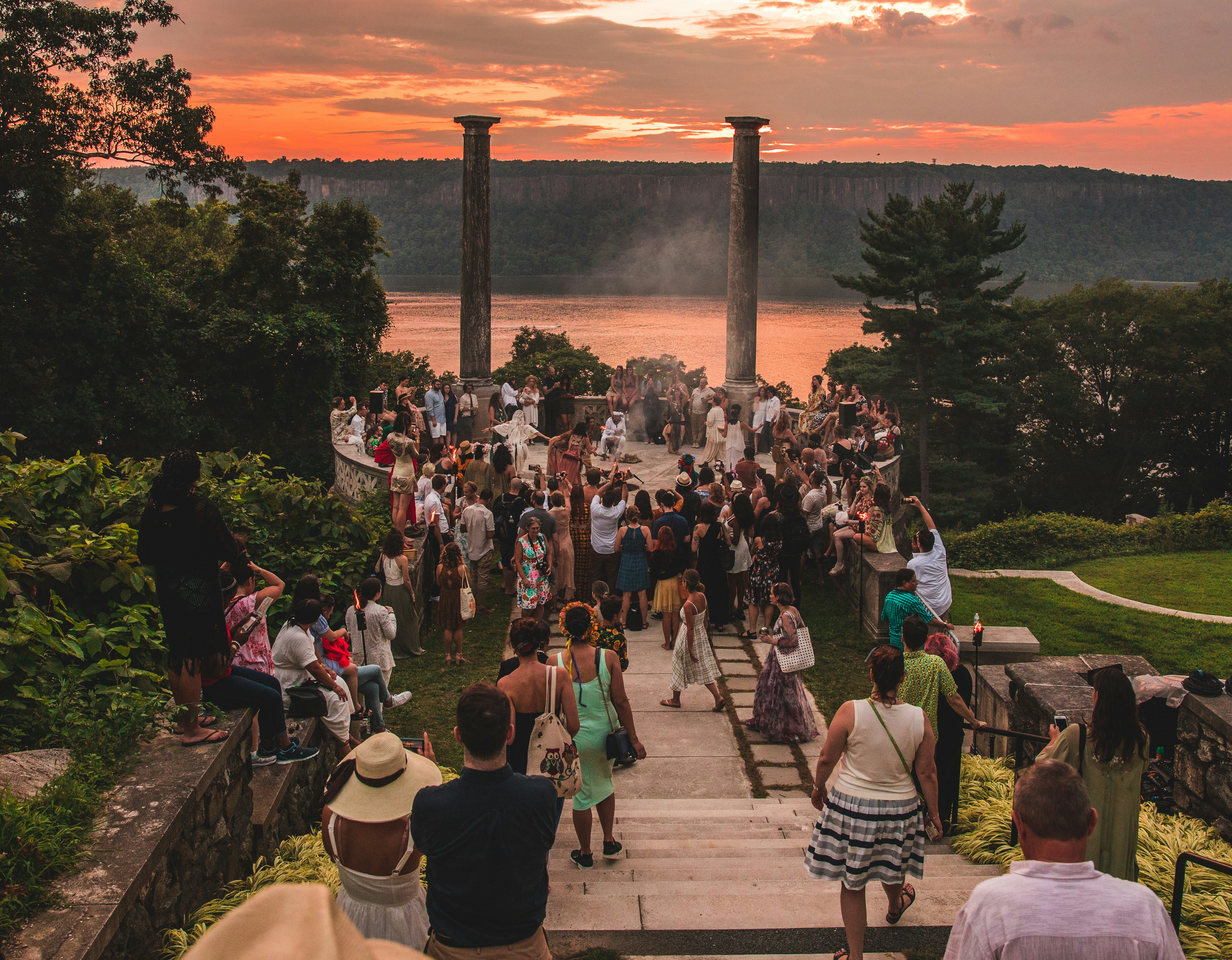 Crowd gathered at Untermyer Park and Gardens during sunset, with vibrant sky and distant columns framing the scene.