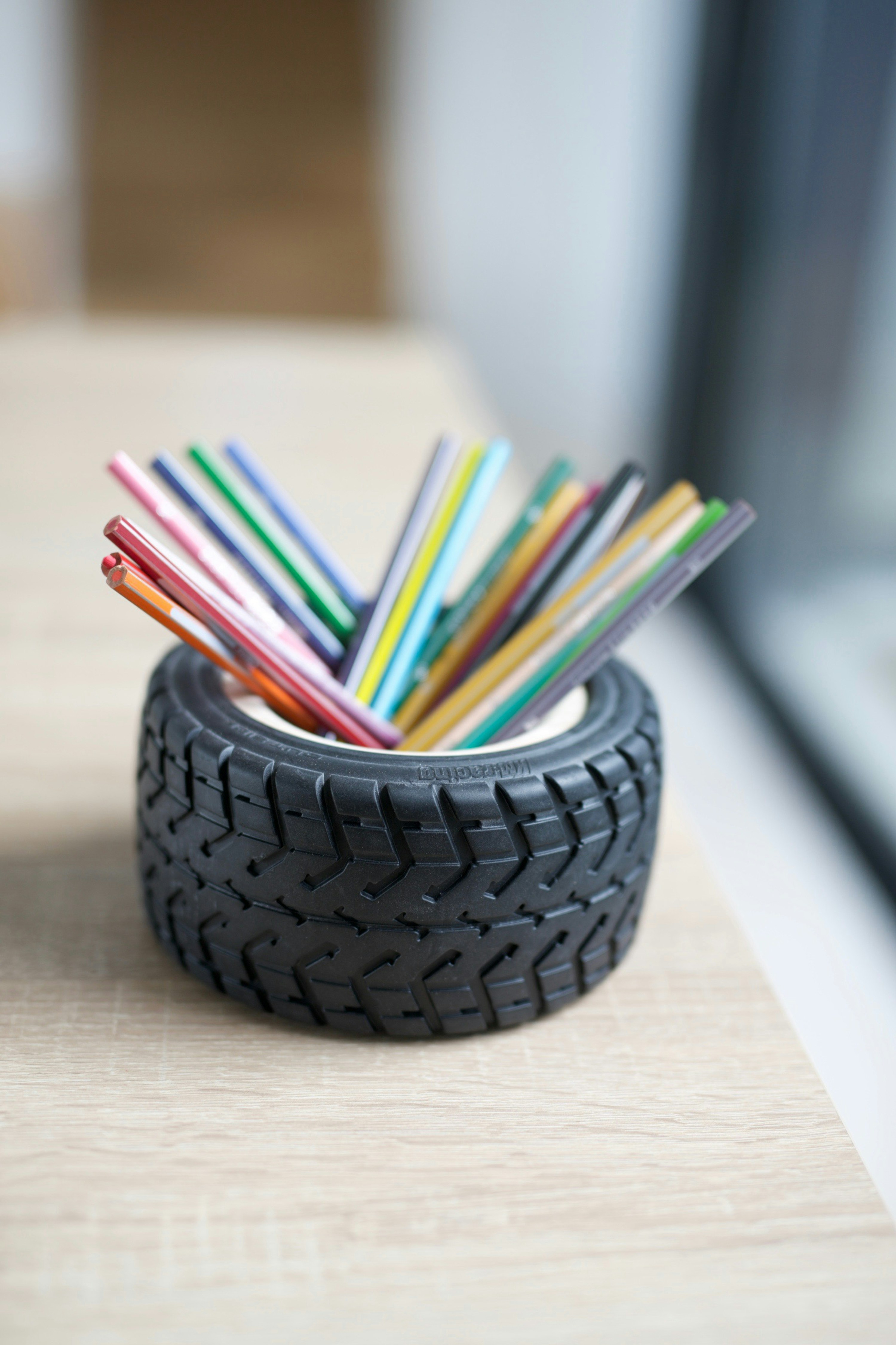 Colorful pencils arranged in a black tire-shaped container on a wooden surface.