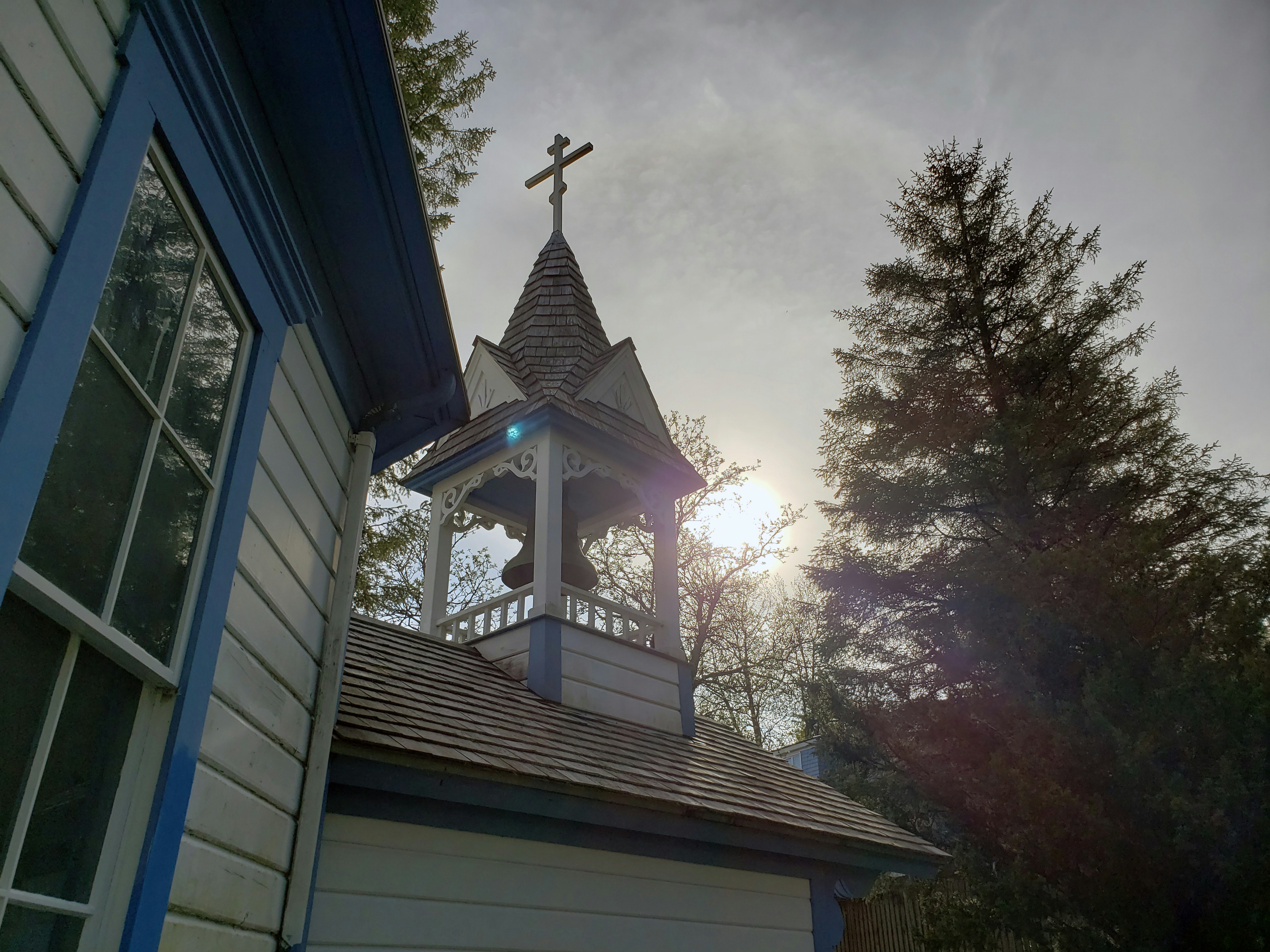 Cross-Topped Bell Tower Bathed in Sunlight Among Blue Siding