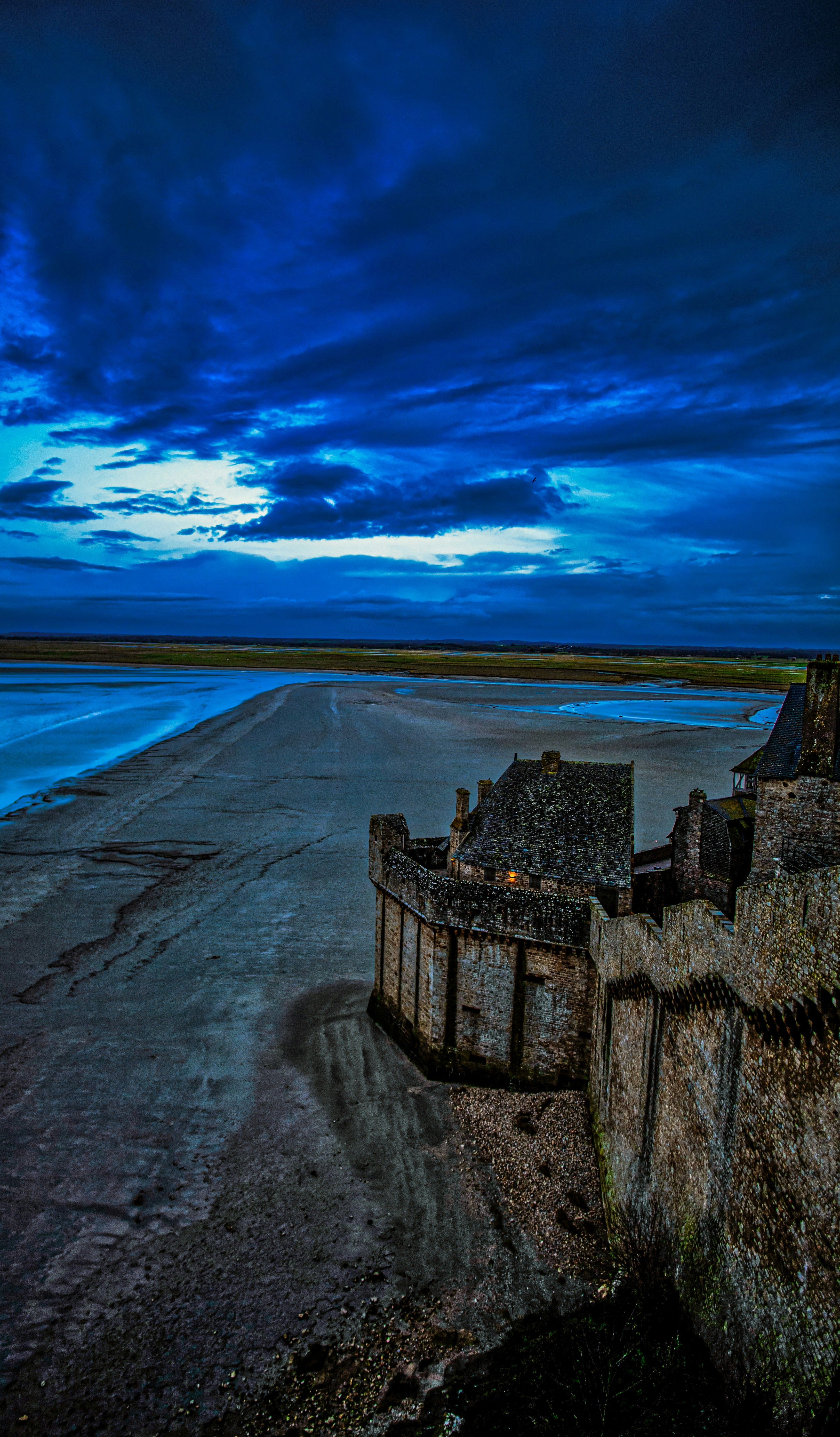 Ancient stone fort overlooking a vast, empty beach under a dramatic blue evening sky.