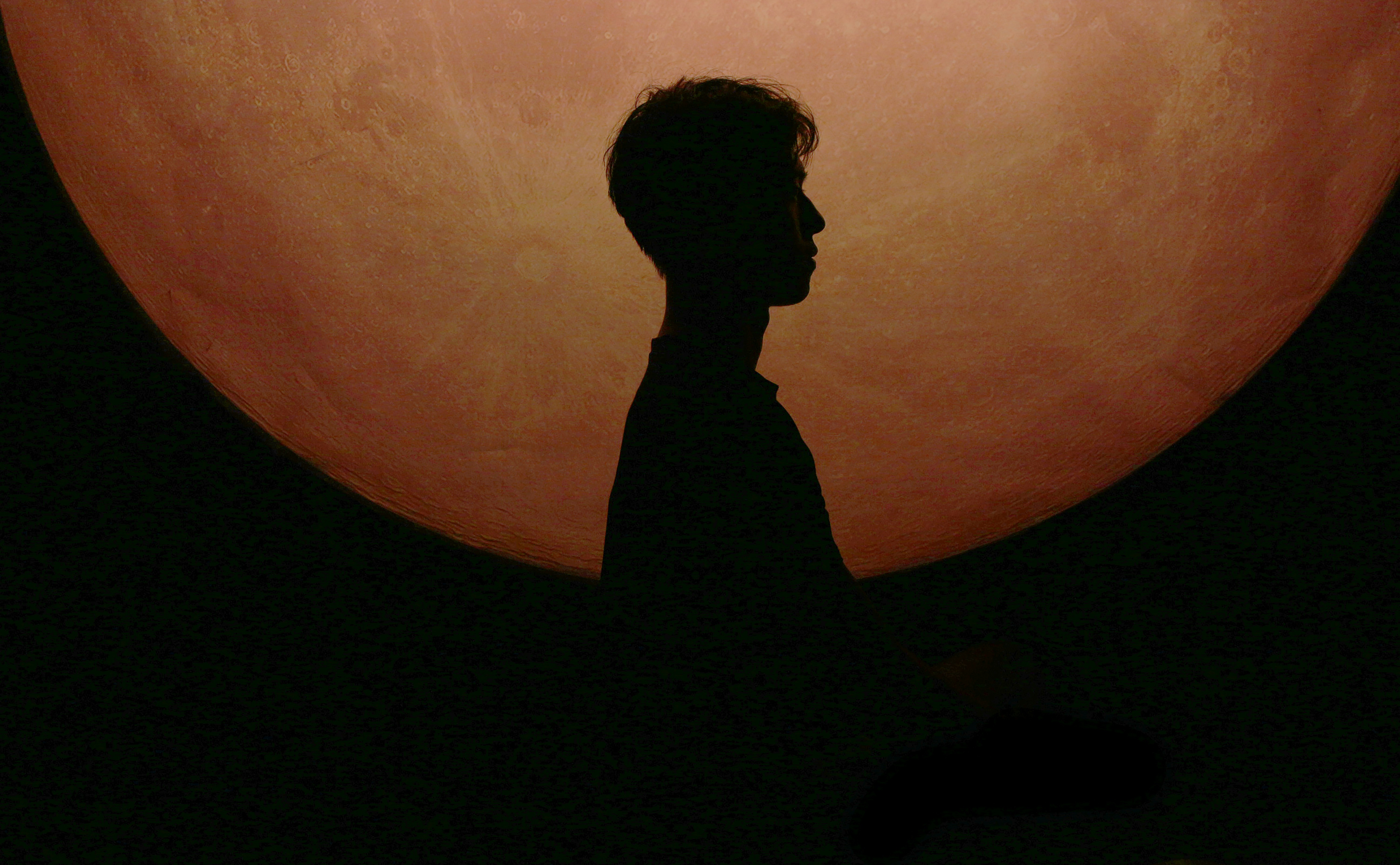 Silhouette against a lunar red glow: a lone figure before a celestial orb
