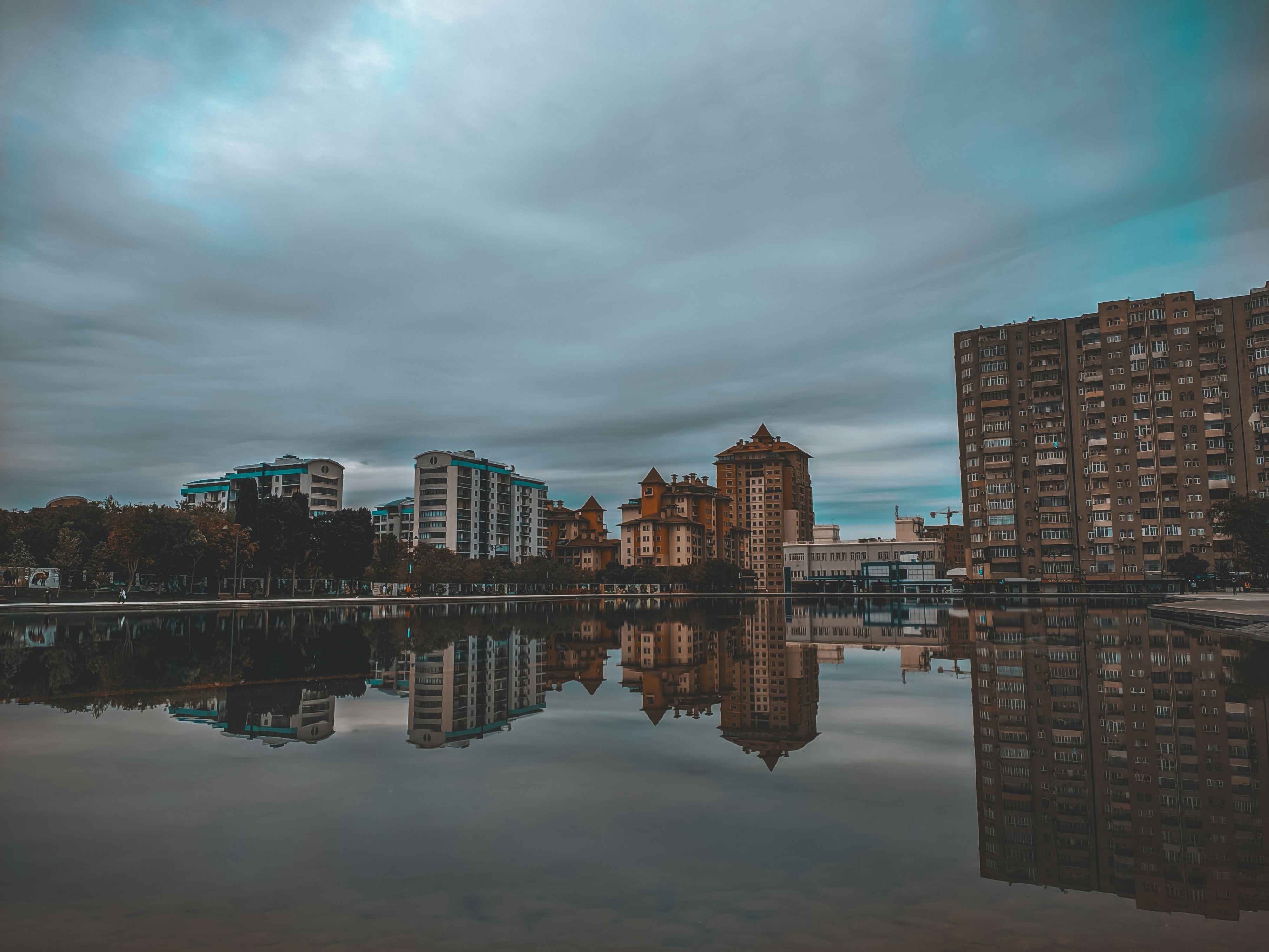 A tranquil scene showcasing a city skyline mirrored in calm waters under a moody sky.