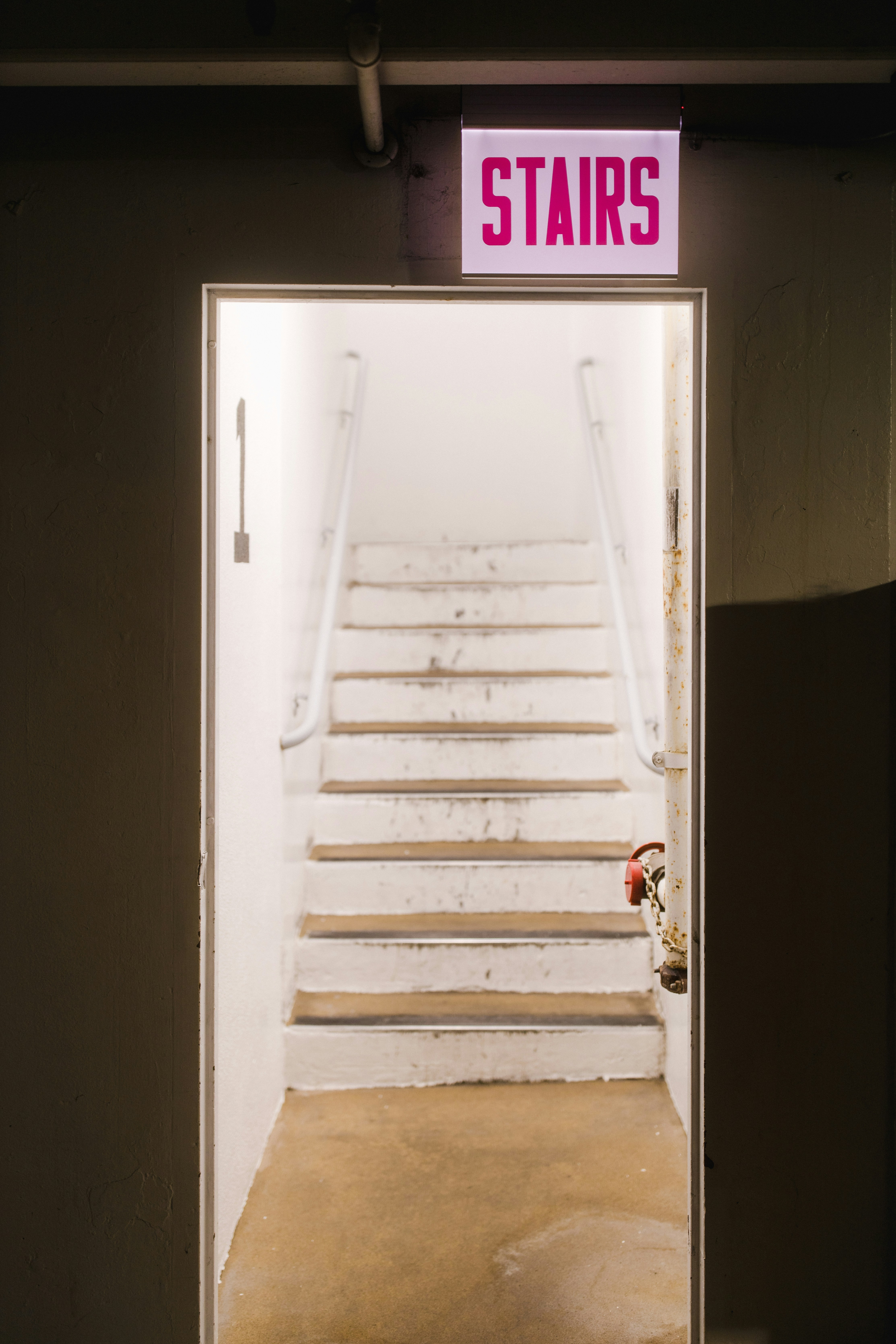 Threshold of Light: The Pink Sign Above a Stairwell in Shadow
