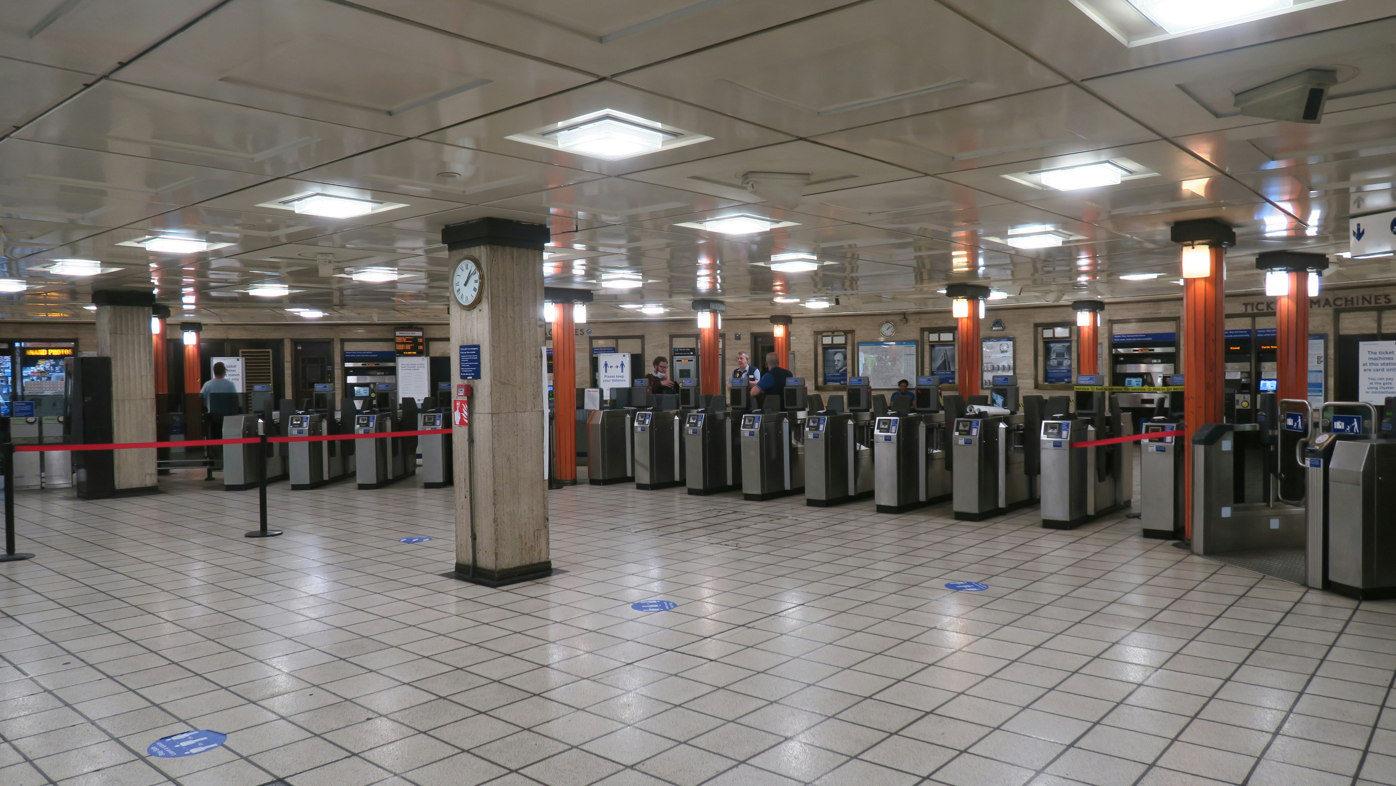 Empty ticket barriers in a transit station, highlighting the organized layout and ambient lighting. A clock on the wall indicates the passage of time.
