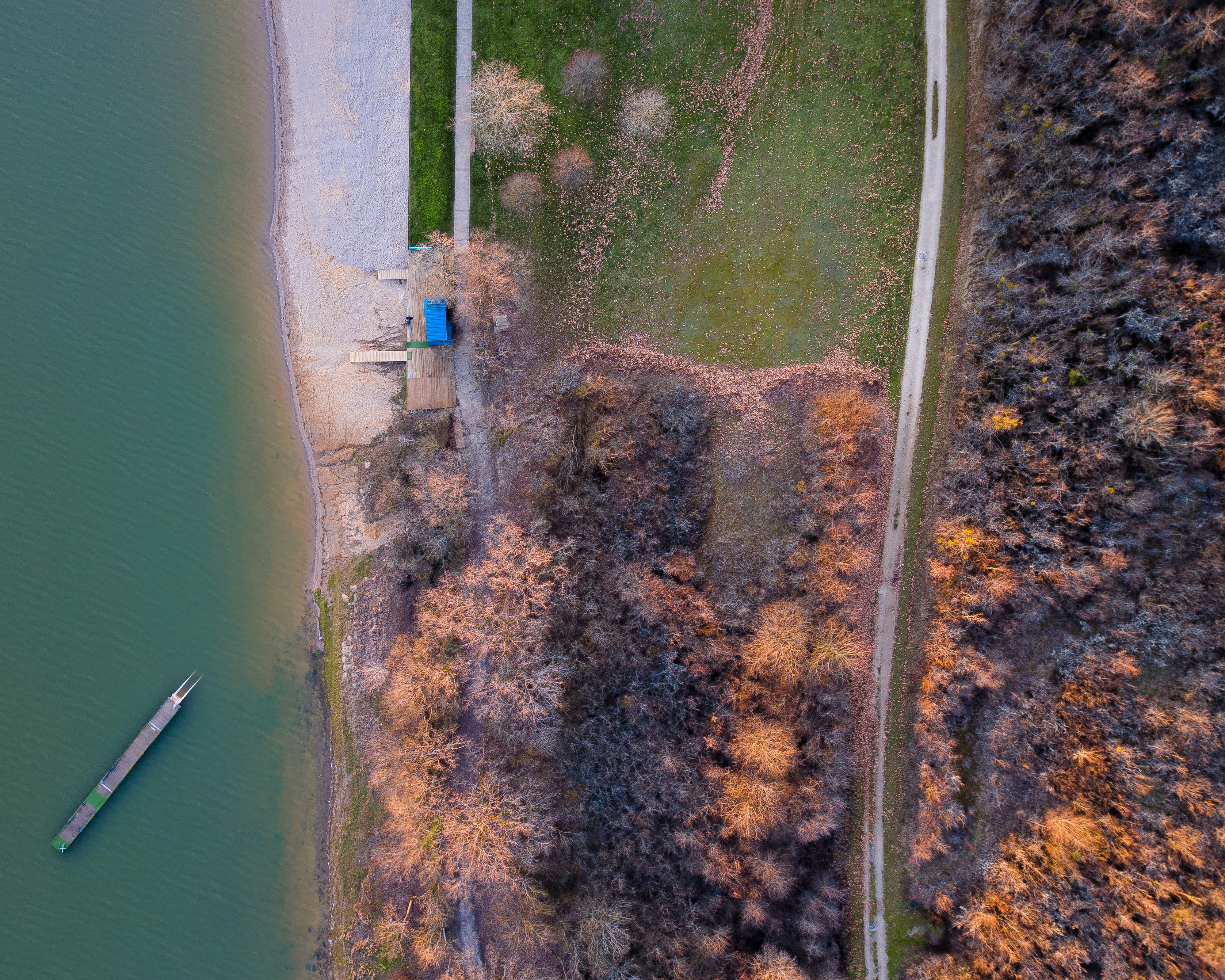 Aerial view of Lac de la Liez displaying contrasting textures of water, grass, and autumnal trees.