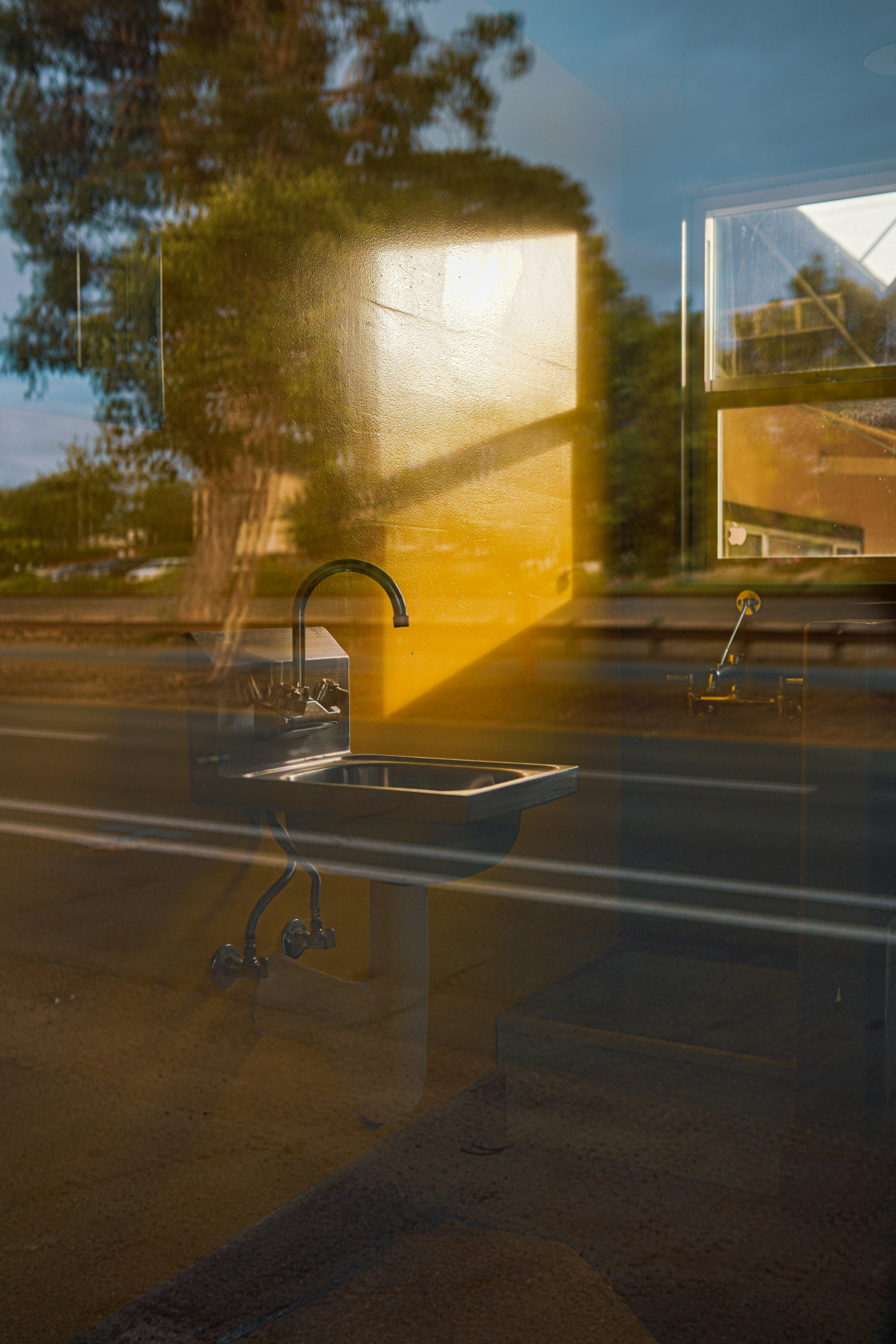 A modern kitchen sink reflected in a window, capturing the interplay of light and surroundings. The vibrant yellow wall adds a unique contrast to the scene.