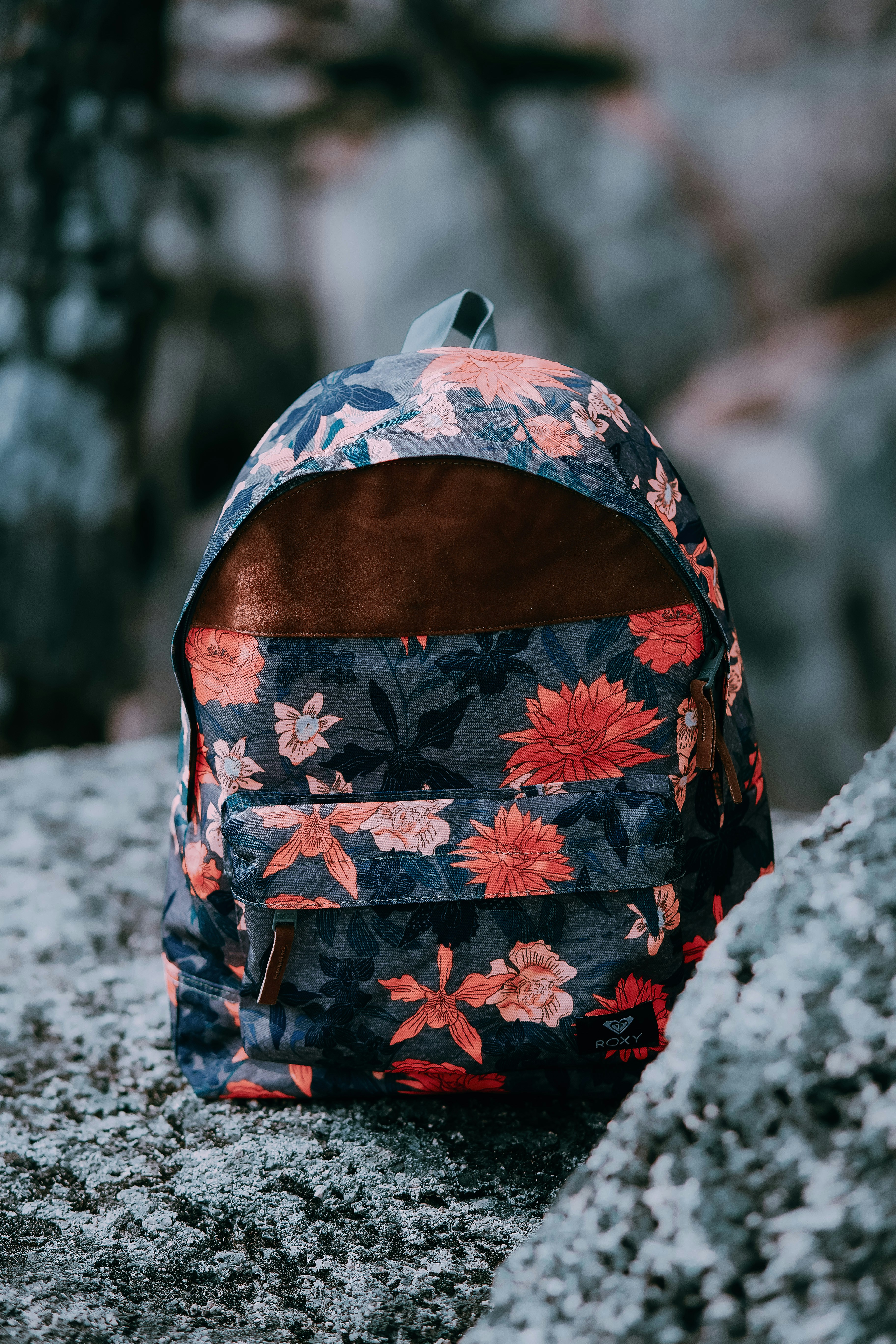Floral-patterned backpack resting on a rocky surface, showcasing vibrant colors against a blurred natural backdrop.