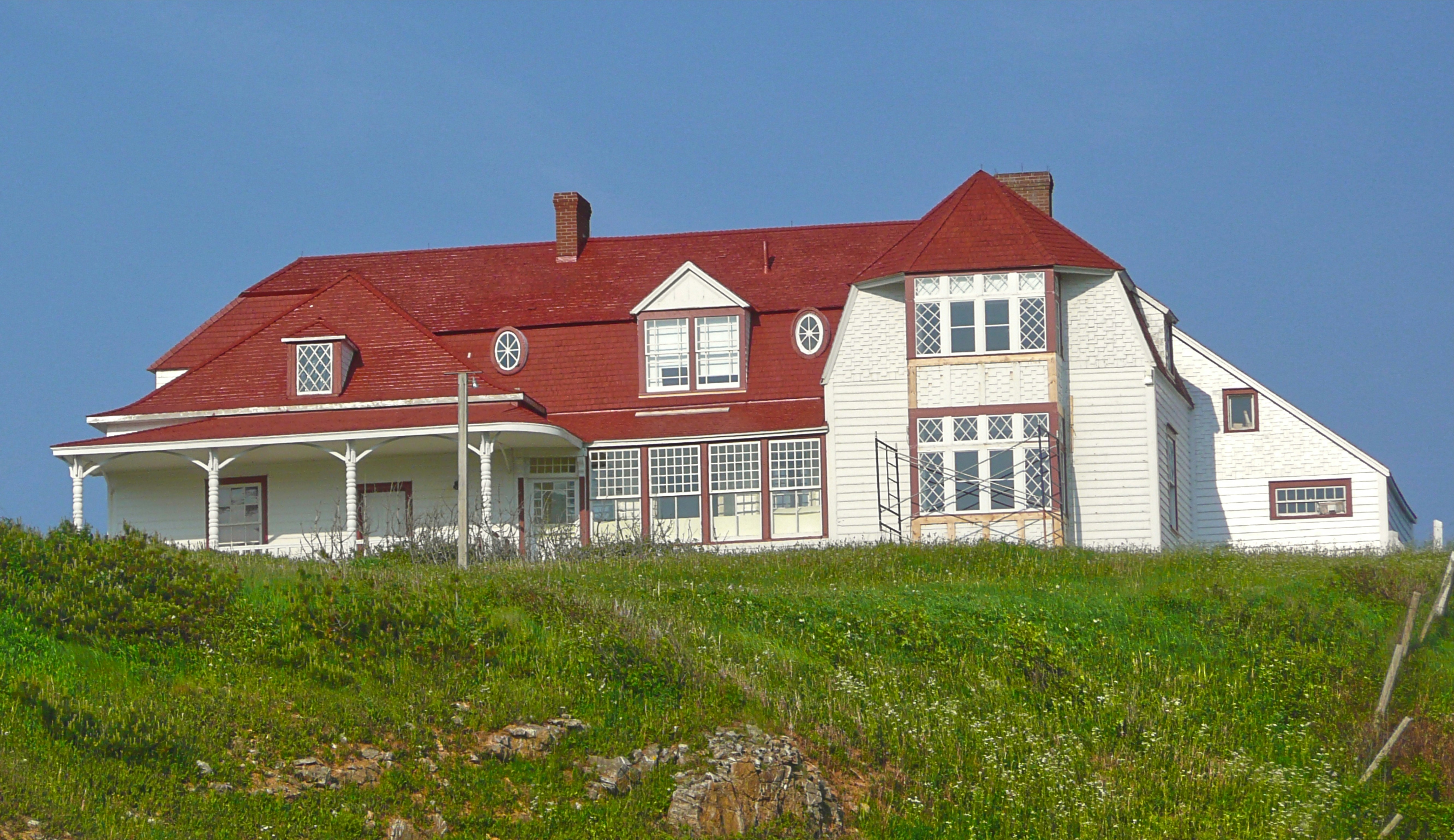 Hilltop white house with a vivid red roof sits on a grassy slope under a clear blue sky.