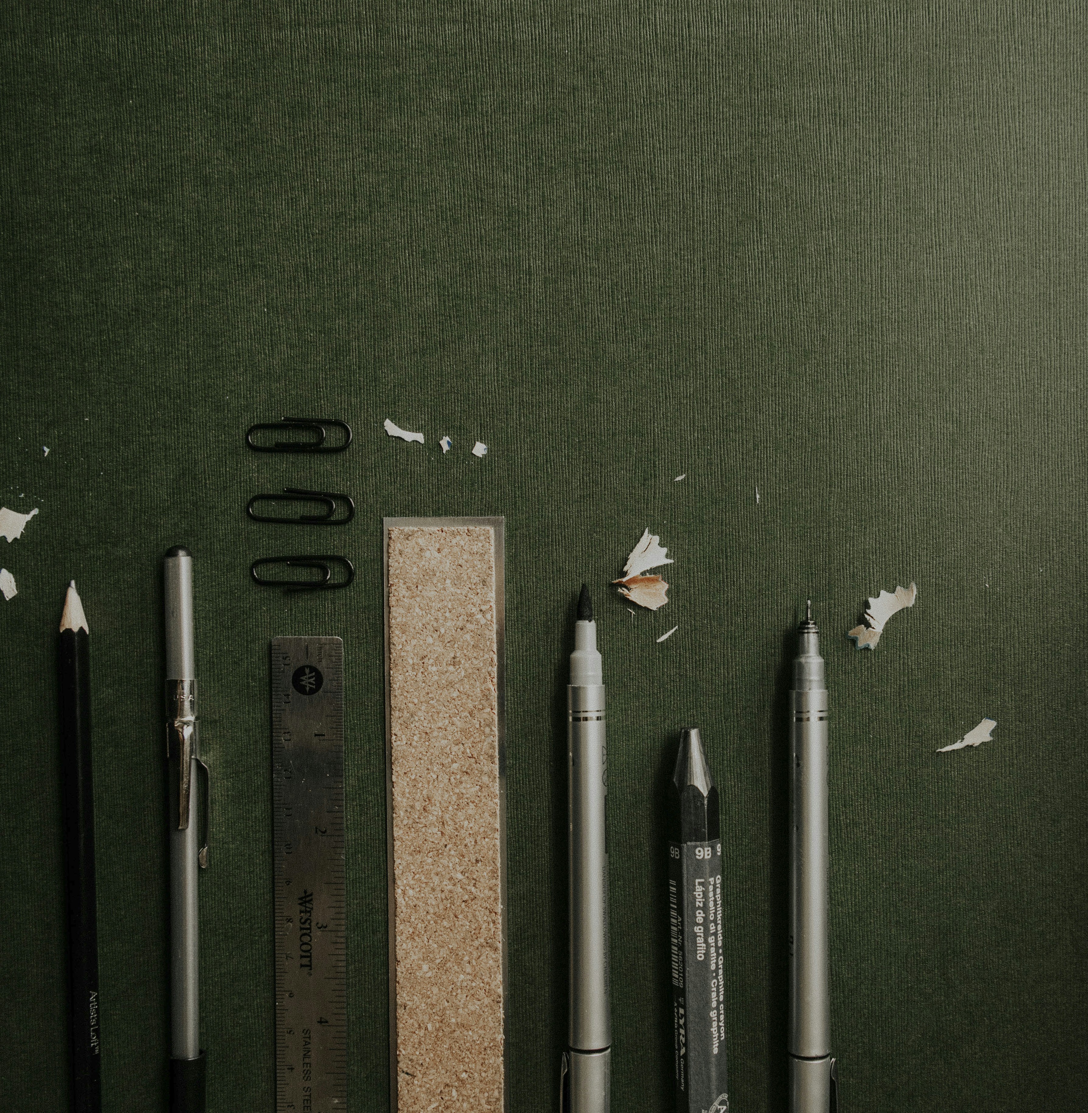 A neatly arranged collection of drawing and writing tools on a textured green surface, showcasing creativity in action.