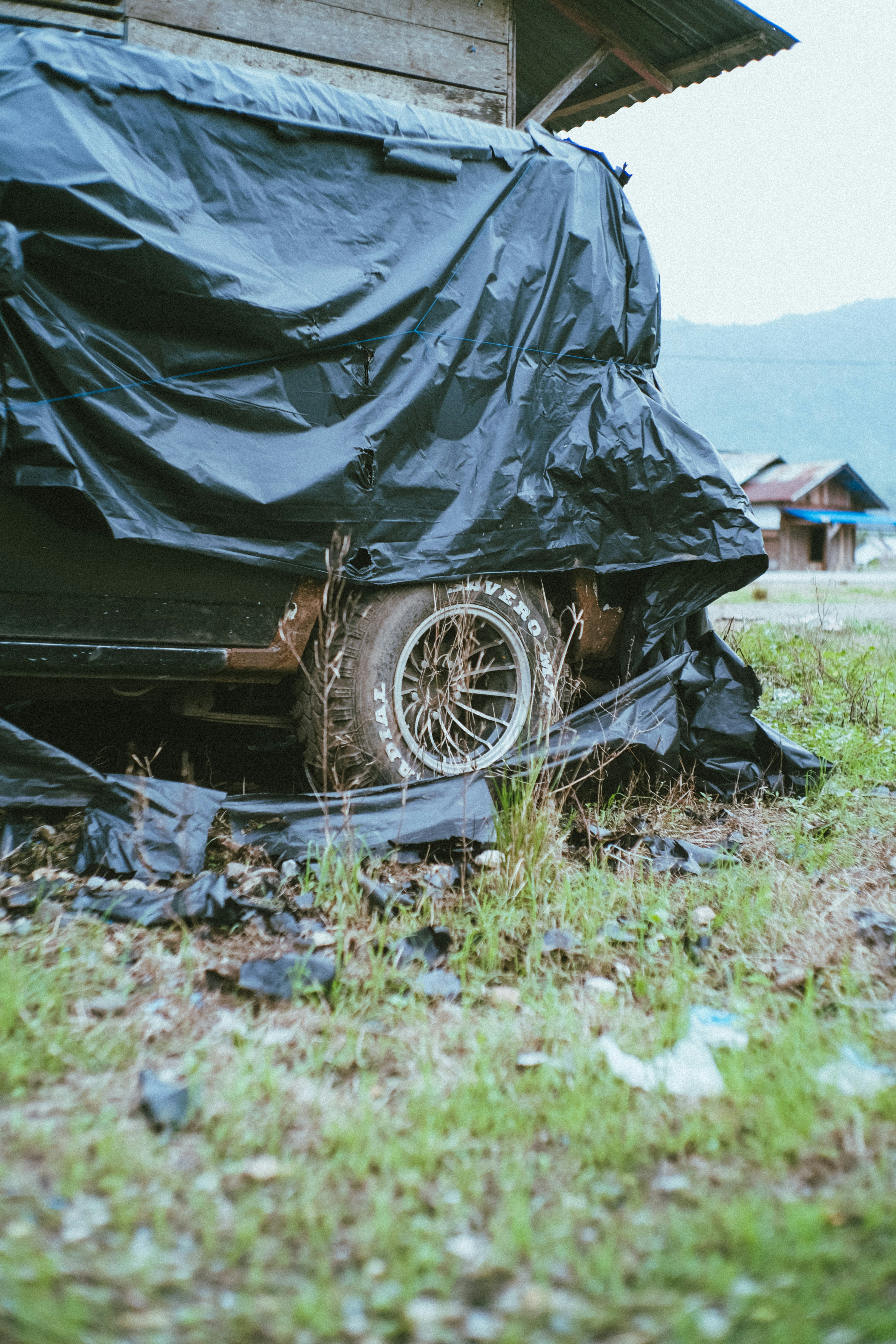 Tarped relic: a weathered wheel peeks from a rural car