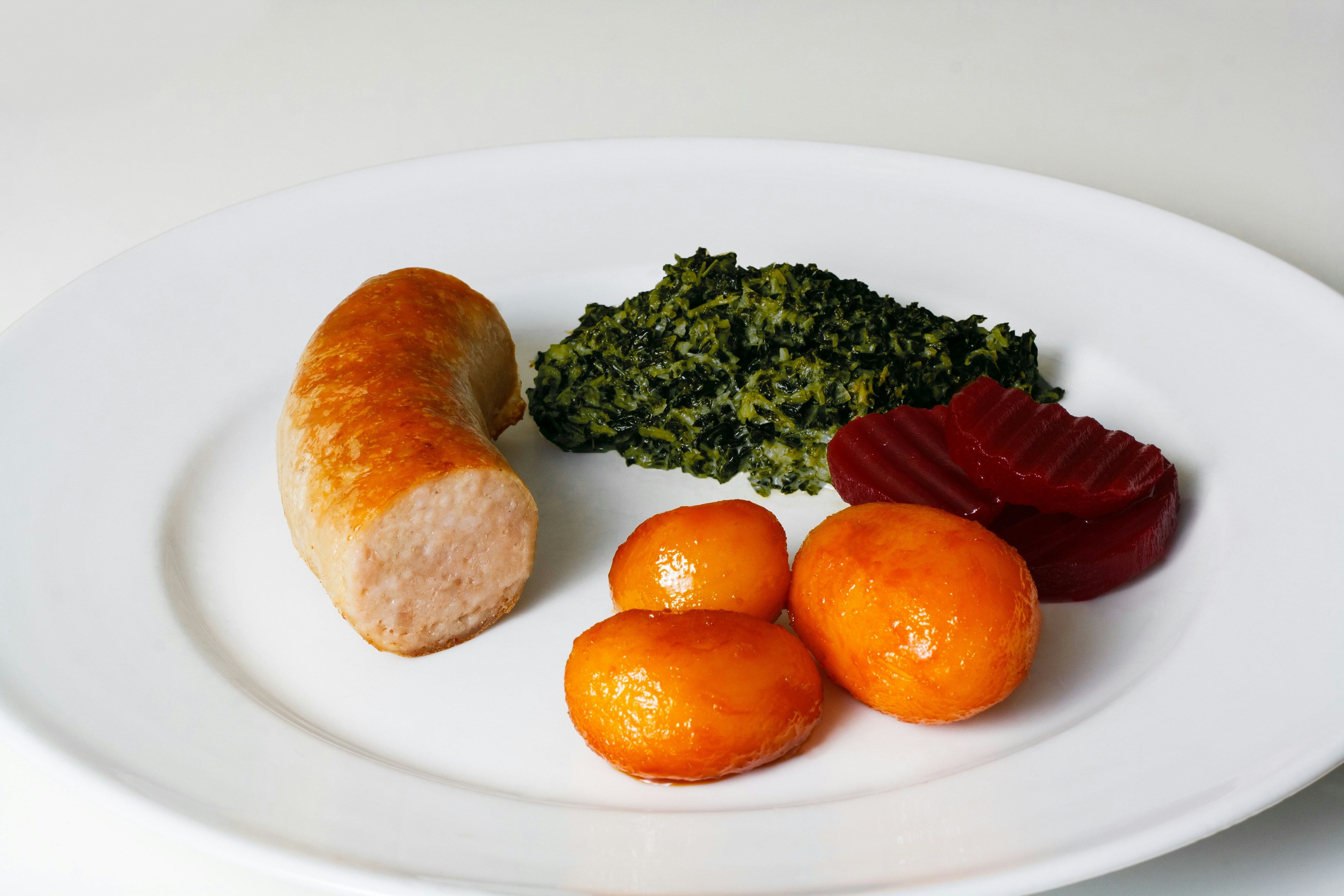 Curved sausage, emerald kale, and amber pearl potatoes on a stark white plate