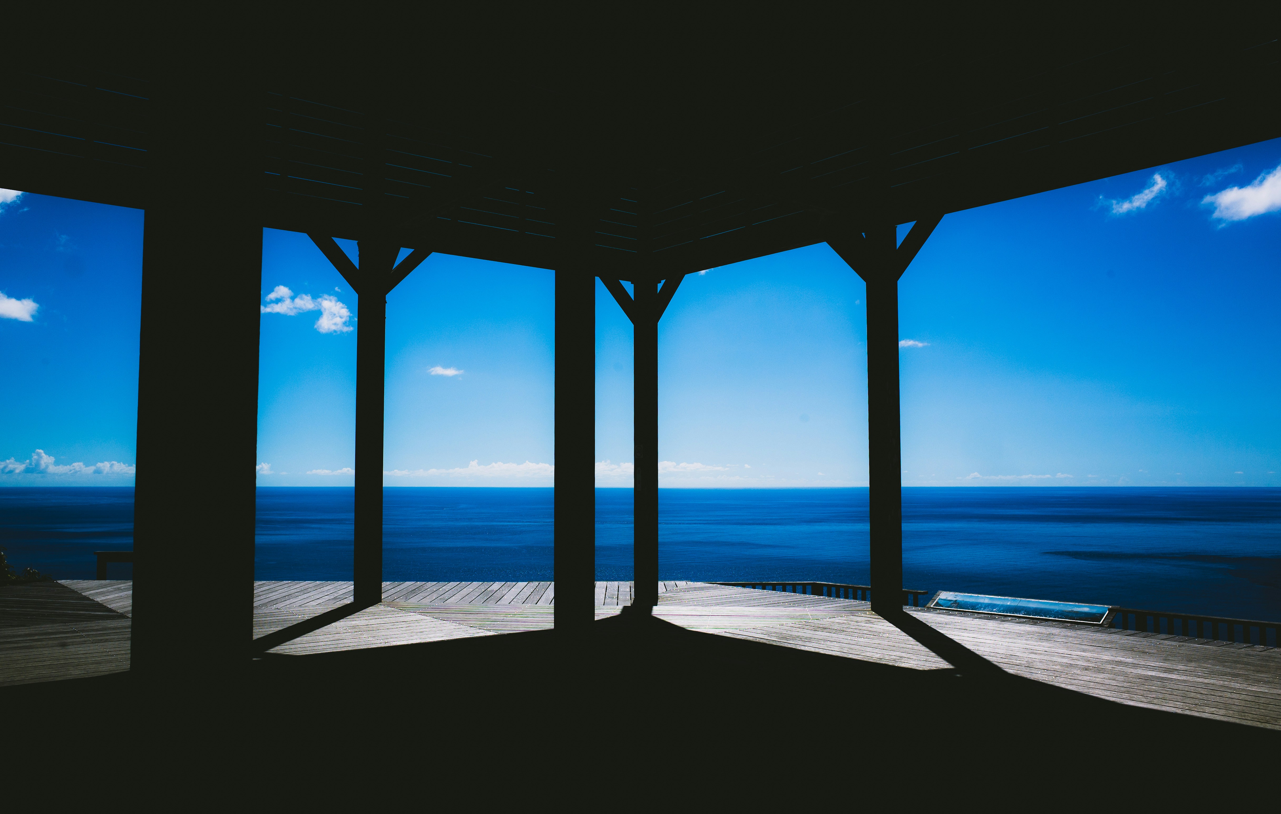 Silhouetted wooden beams create a geometric frame around a tranquil ocean view under a clear blue sky.