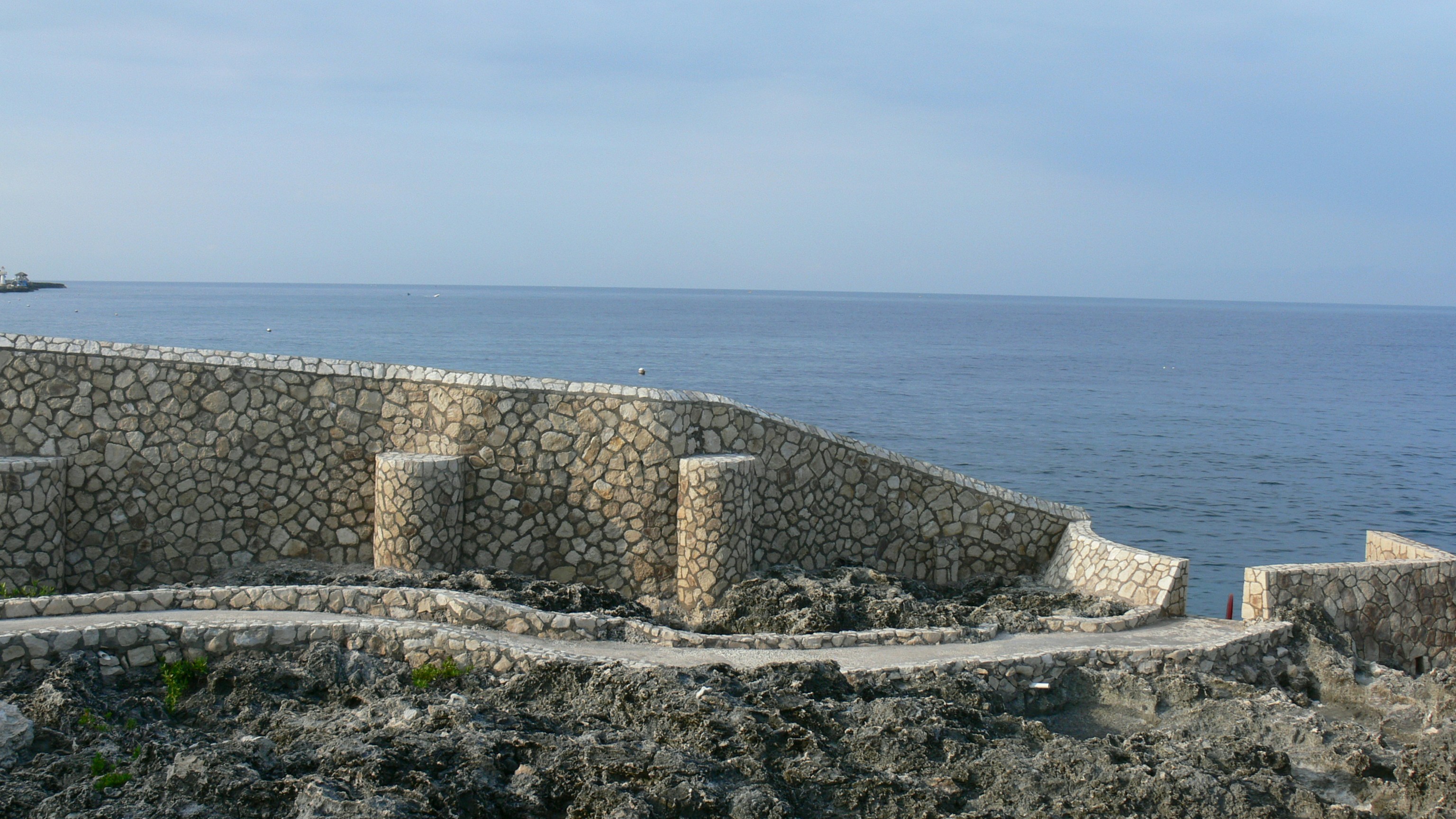 Winding stone pathway leading down to the rocky shoreline, framed by calm ocean waters under a soft sky.
