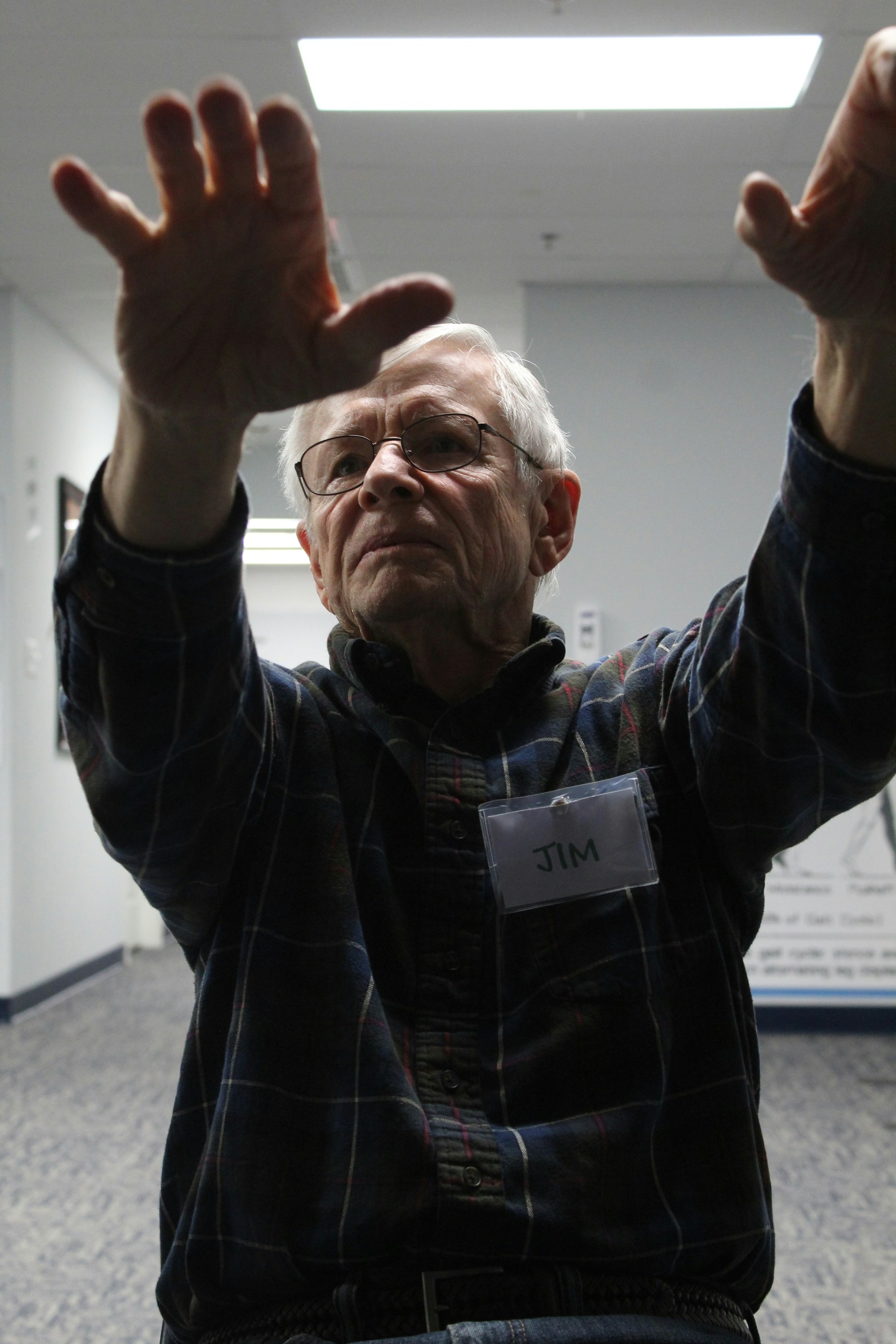 An elderly man extends his hands forward, conveying a sense of engagement and interaction in a softly lit environment.