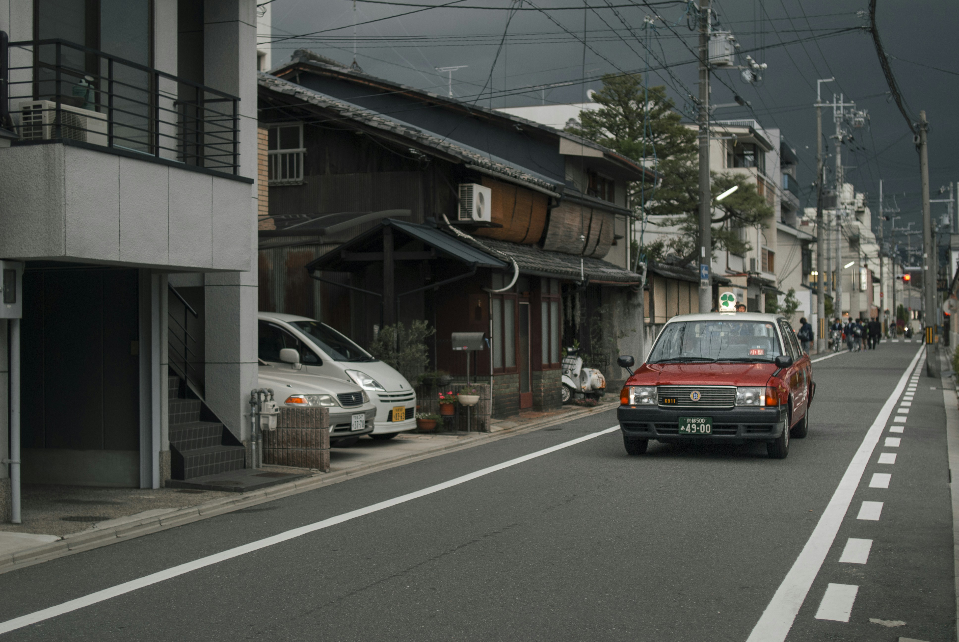 Classic red car navigating a quiet street lined with traditional and modern architecture. The scene captures a blend of urban life and historical charm.