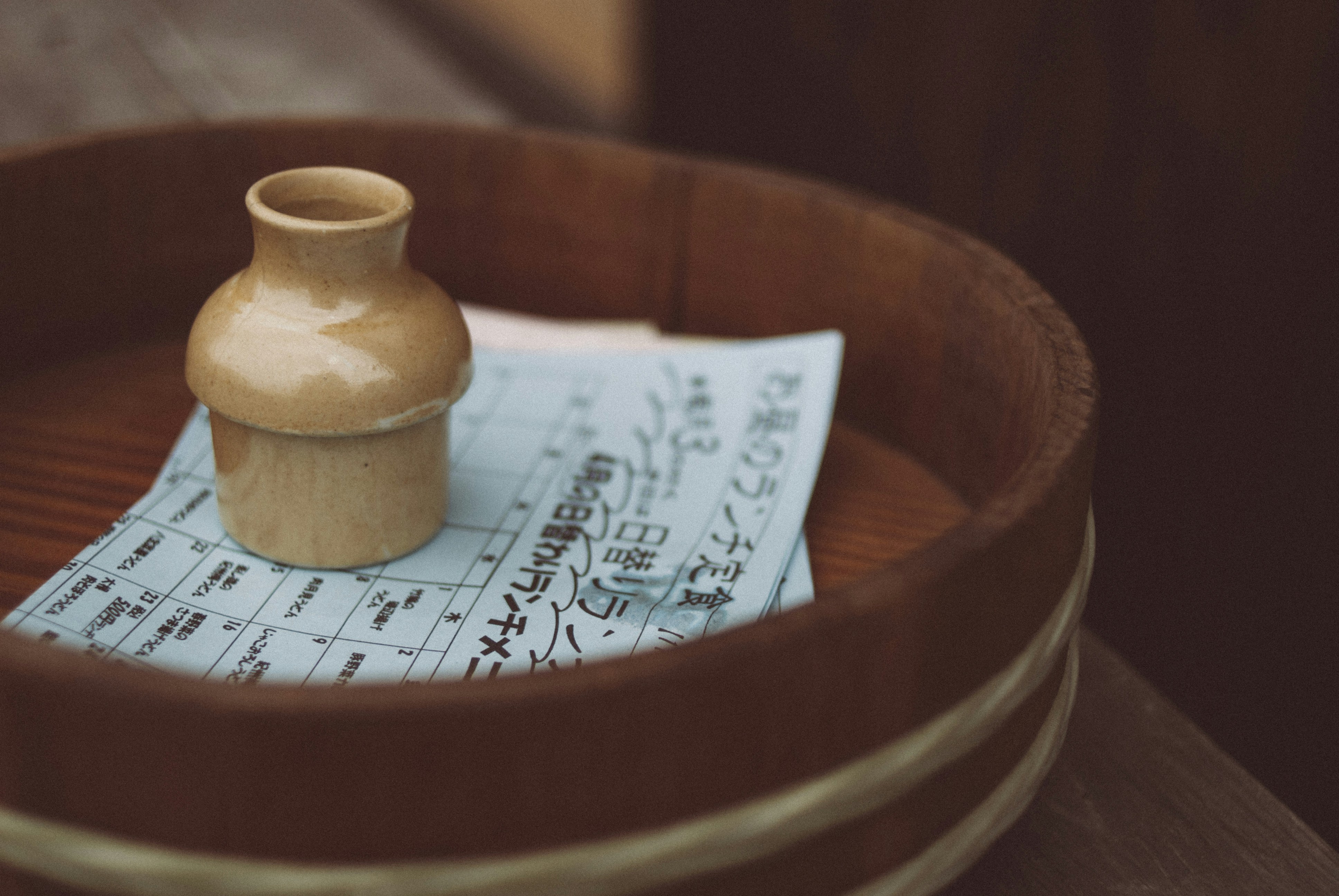 Tiny Earthen Jug Anchored on Printed Pages Inside a Wooden Barrel