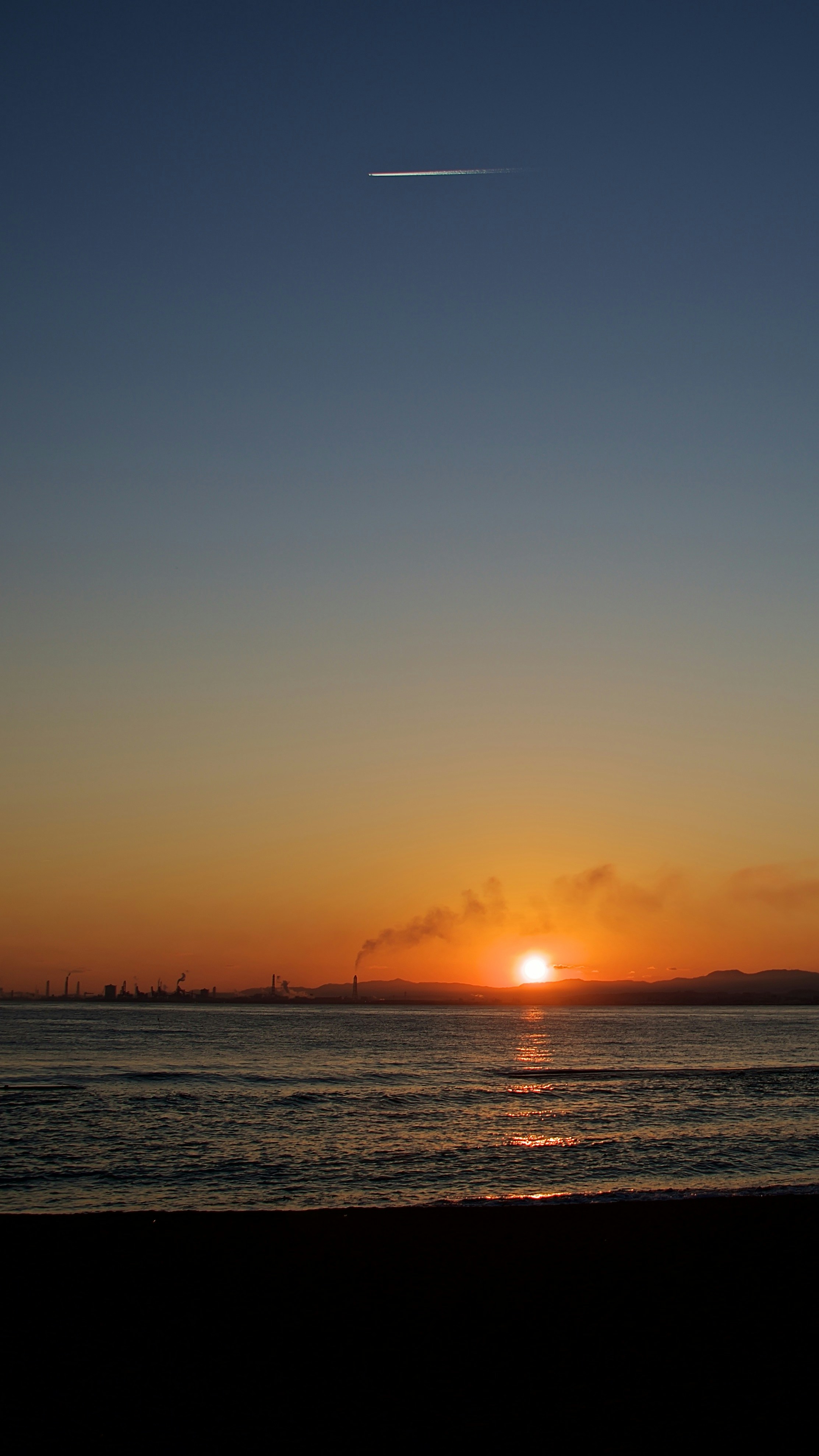 Sunset at the Quiet Edge: Jet Trail Over a Distant Industrial Horizon