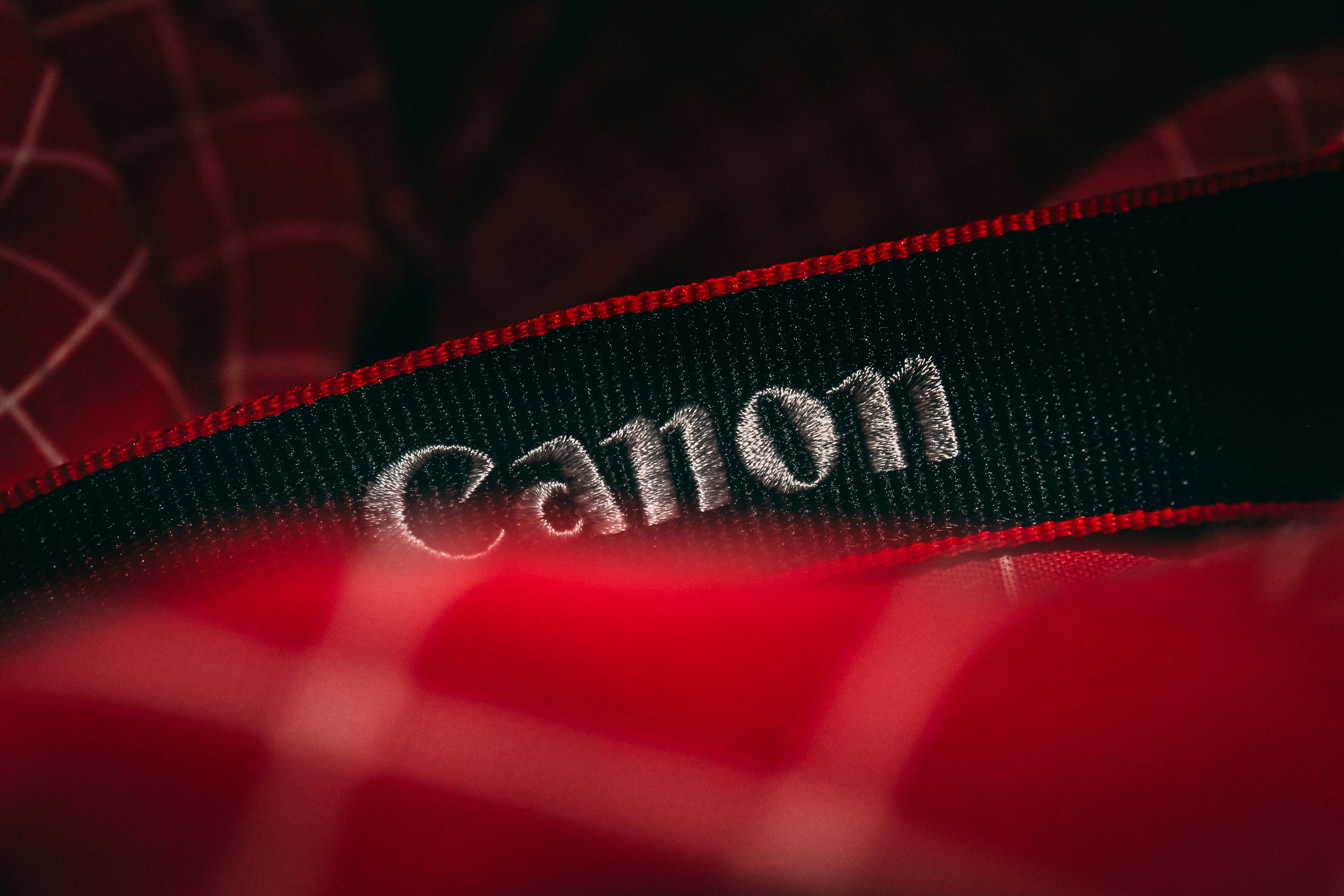 Close-up of a Canon camera strap resting on a textured red surface, showcasing brand identity and craftsmanship.