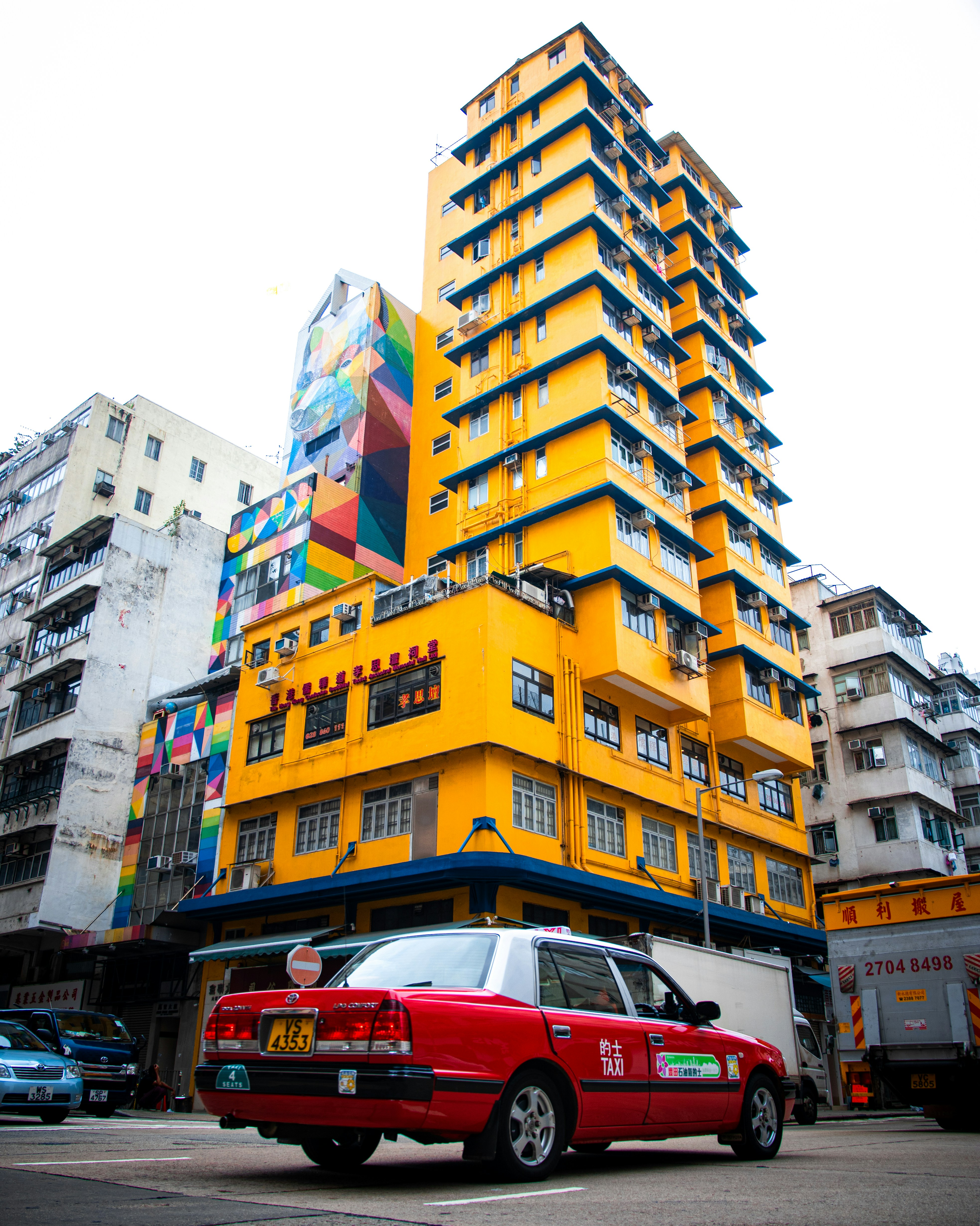 Red taxi passing by classic old yellow building in Hong Kong | red car parked beside yellow concrete building during daytime