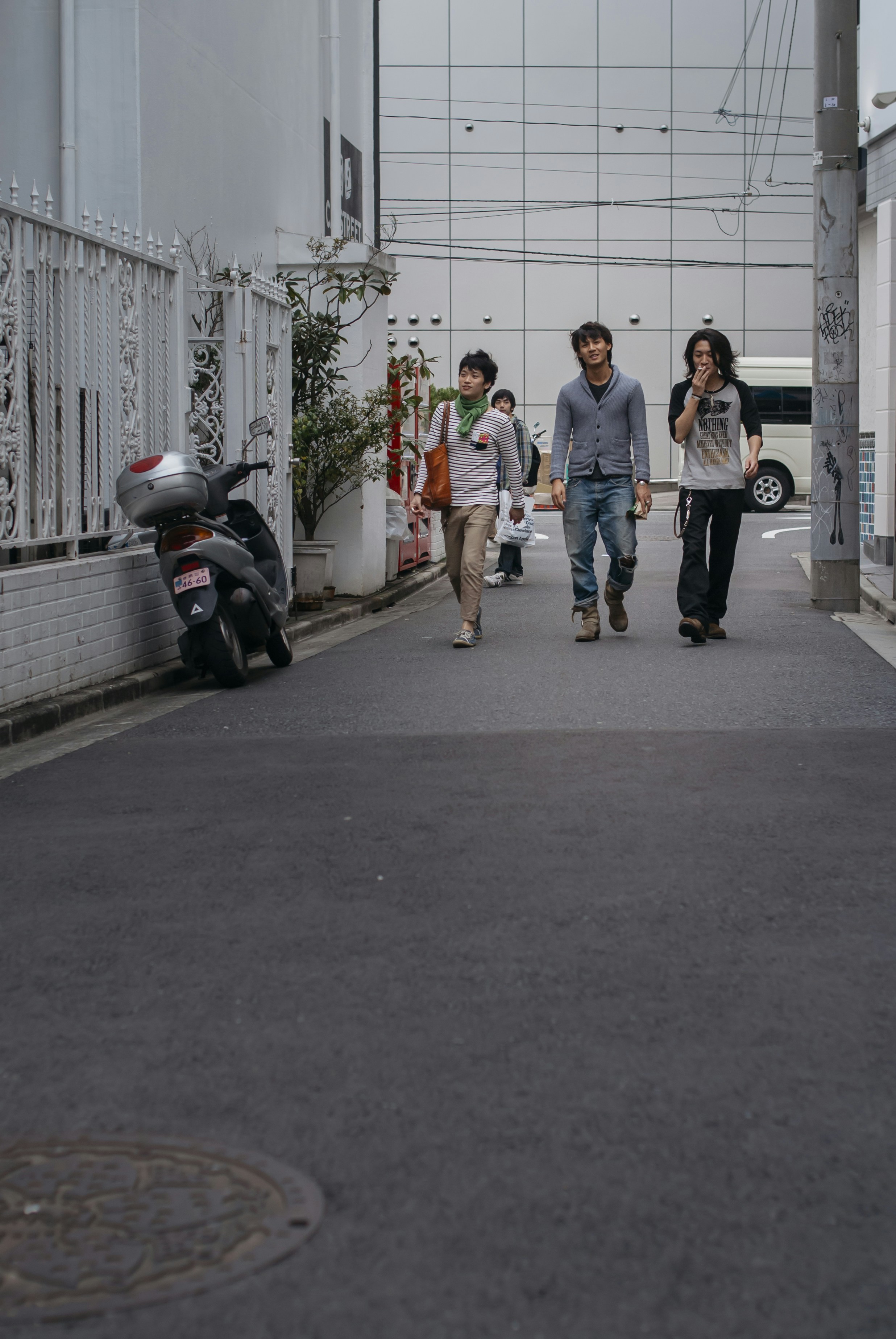 Three individuals walking down a narrow urban alley, surrounded by buildings and parked scooter. A casual scene capturing the essence of city life.