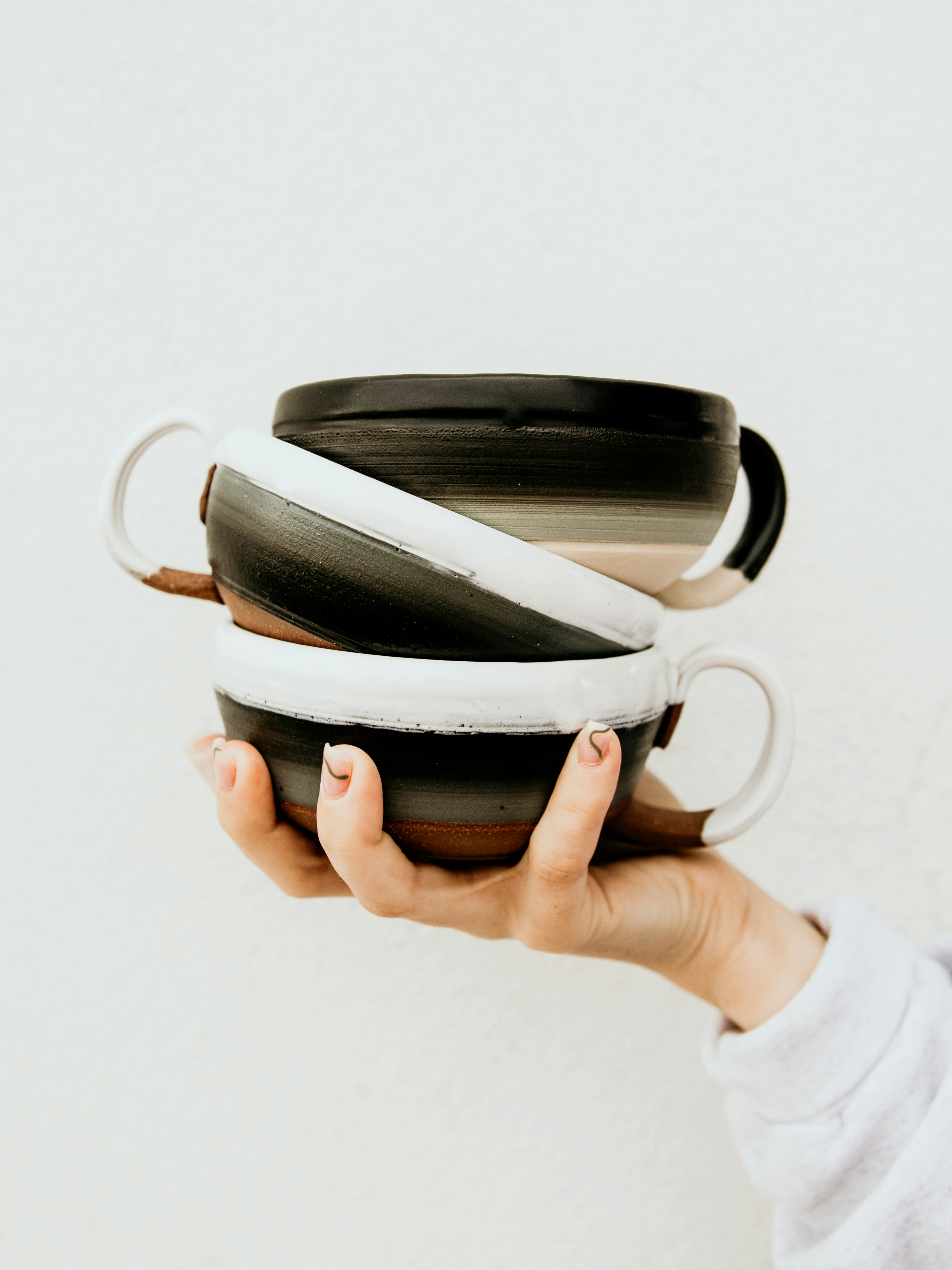 Stack of uniquely designed ceramic bowls held in a hand, showcasing a blend of black, white, and earthy hues against a minimalist background.
