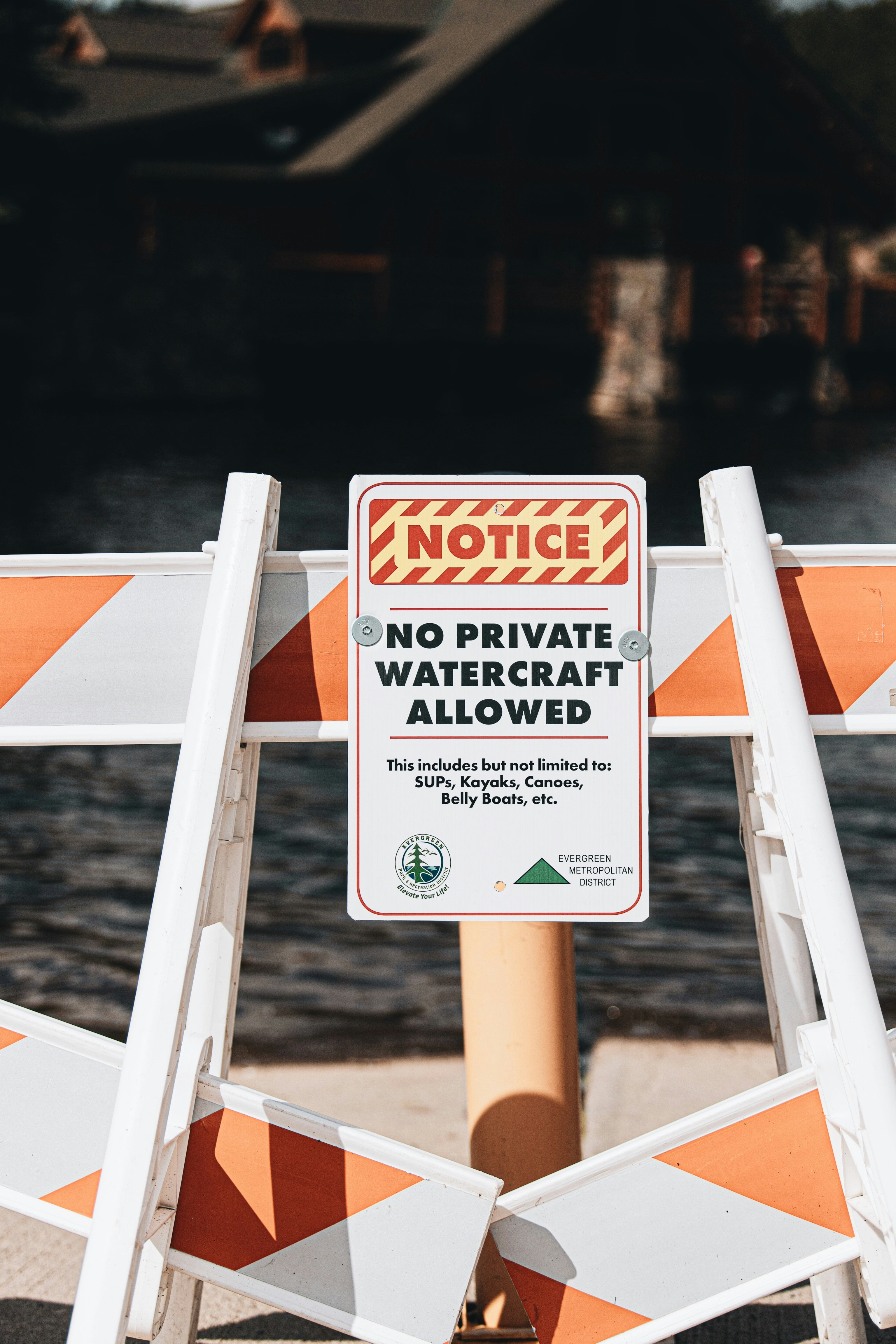Notice Sign Centered Over Orange Barrier by the Water