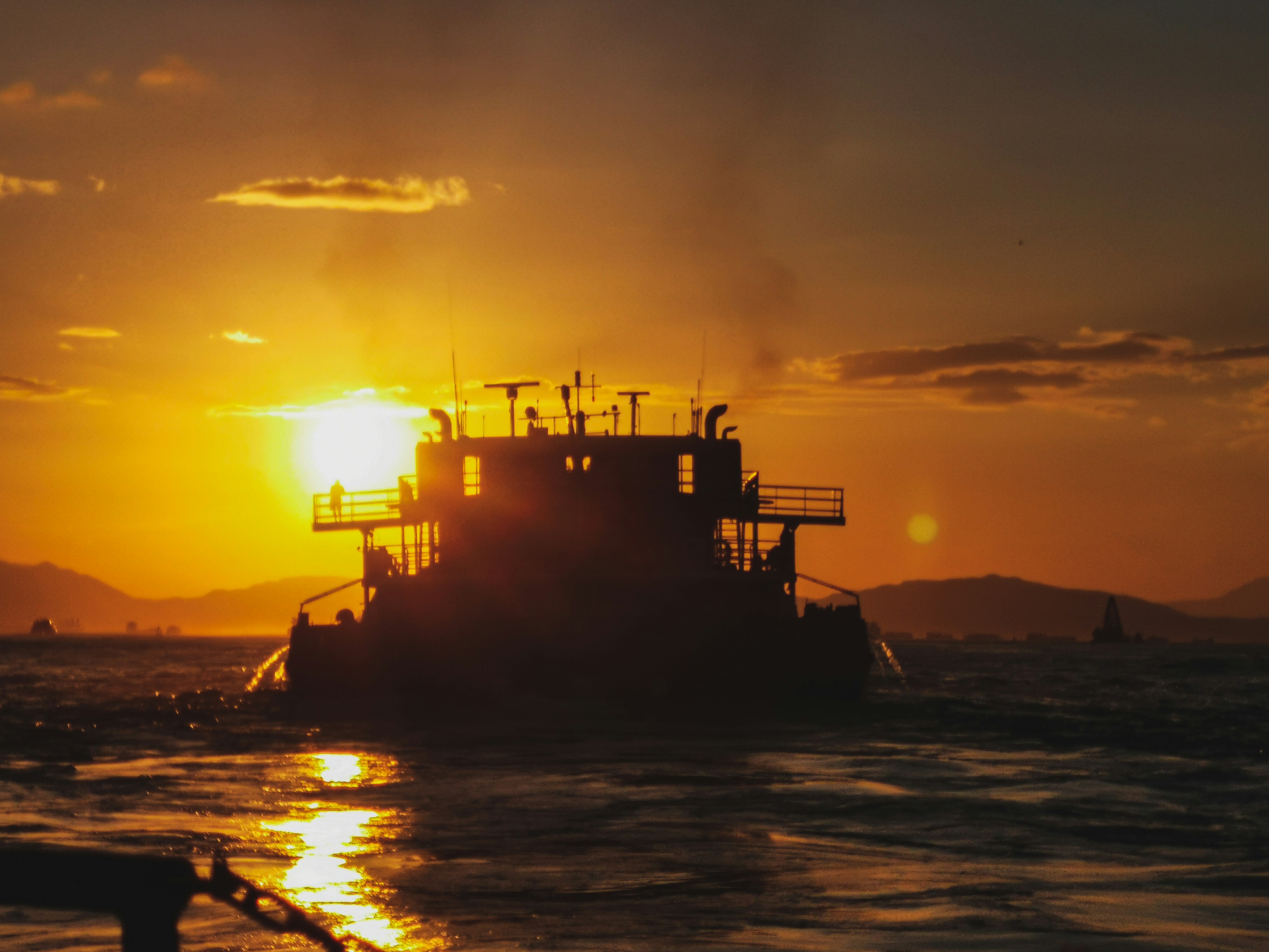 Silhouetted vessel on dark water against a fiery sunset, with a glowing horizon and reflections rippling across the surface.