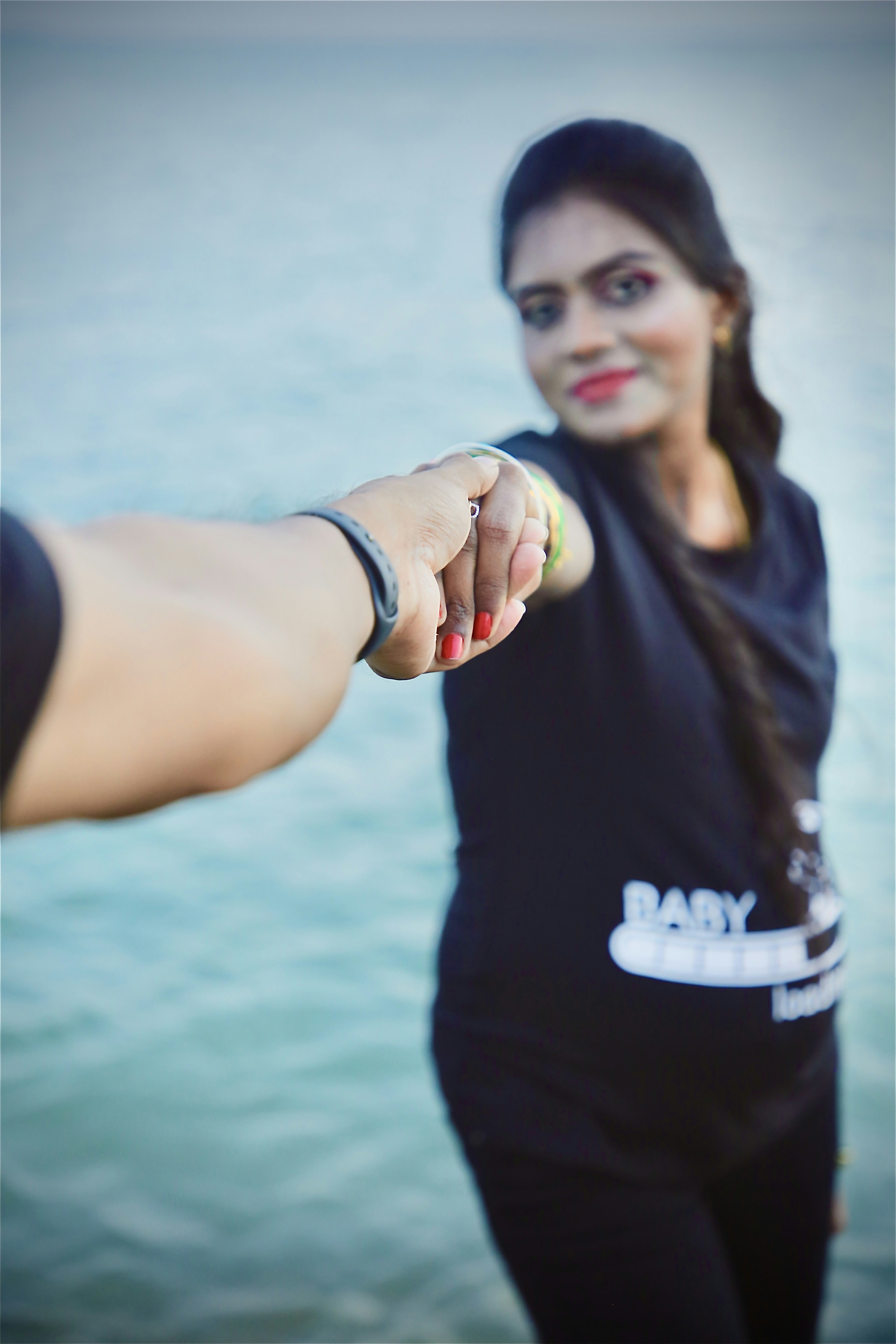 Woman reaching out over a serene water backdrop, holding someone's hand.