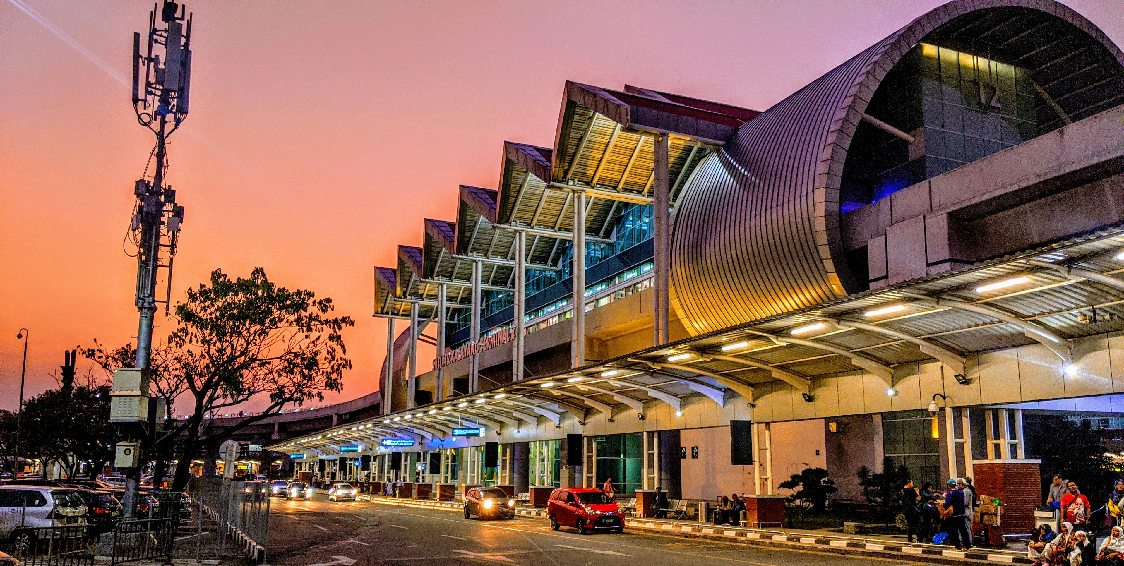 Modern airport facade under a vibrant orange and purple sunset sky.
