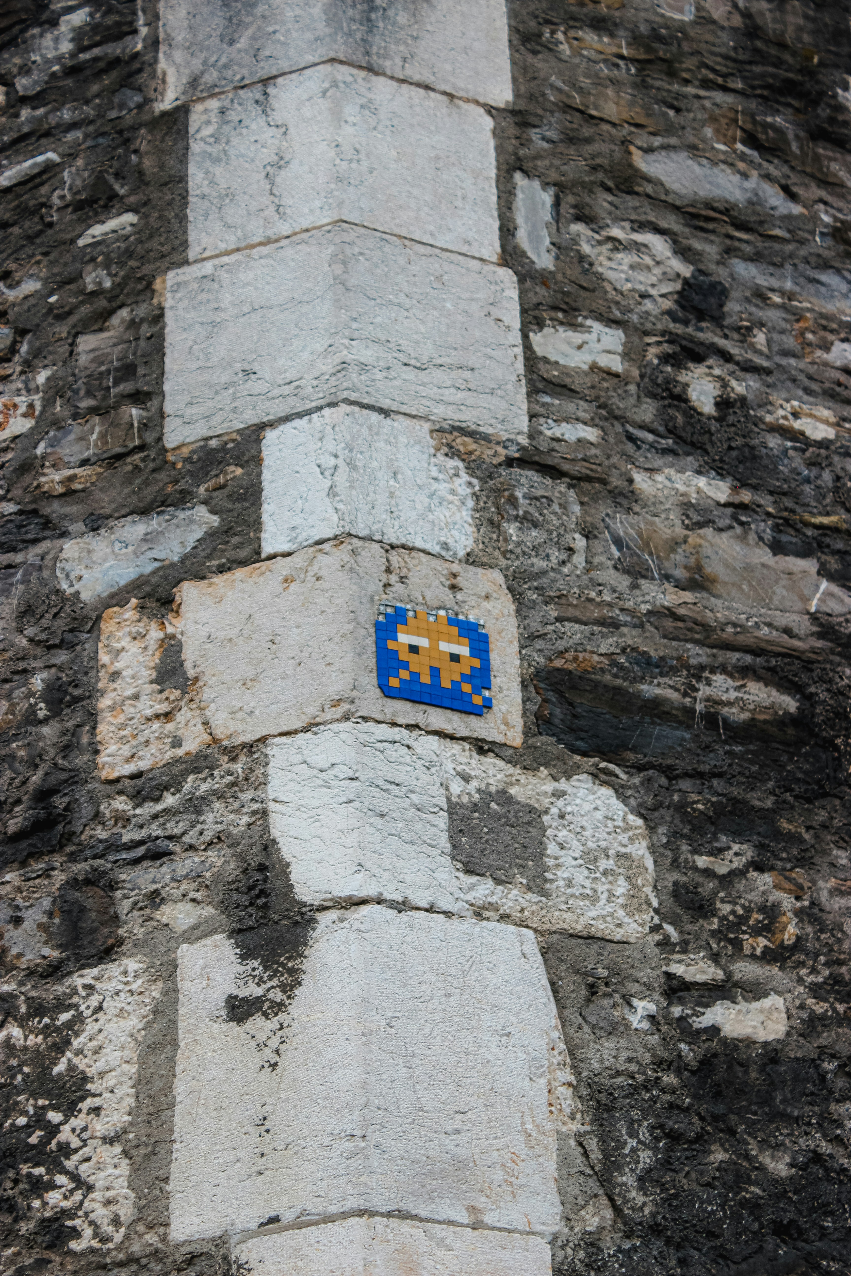 Colorful mosaic tile featuring a pixelated design affixed to a weathered stone wall, showcasing urban art's intersection with historical architecture.