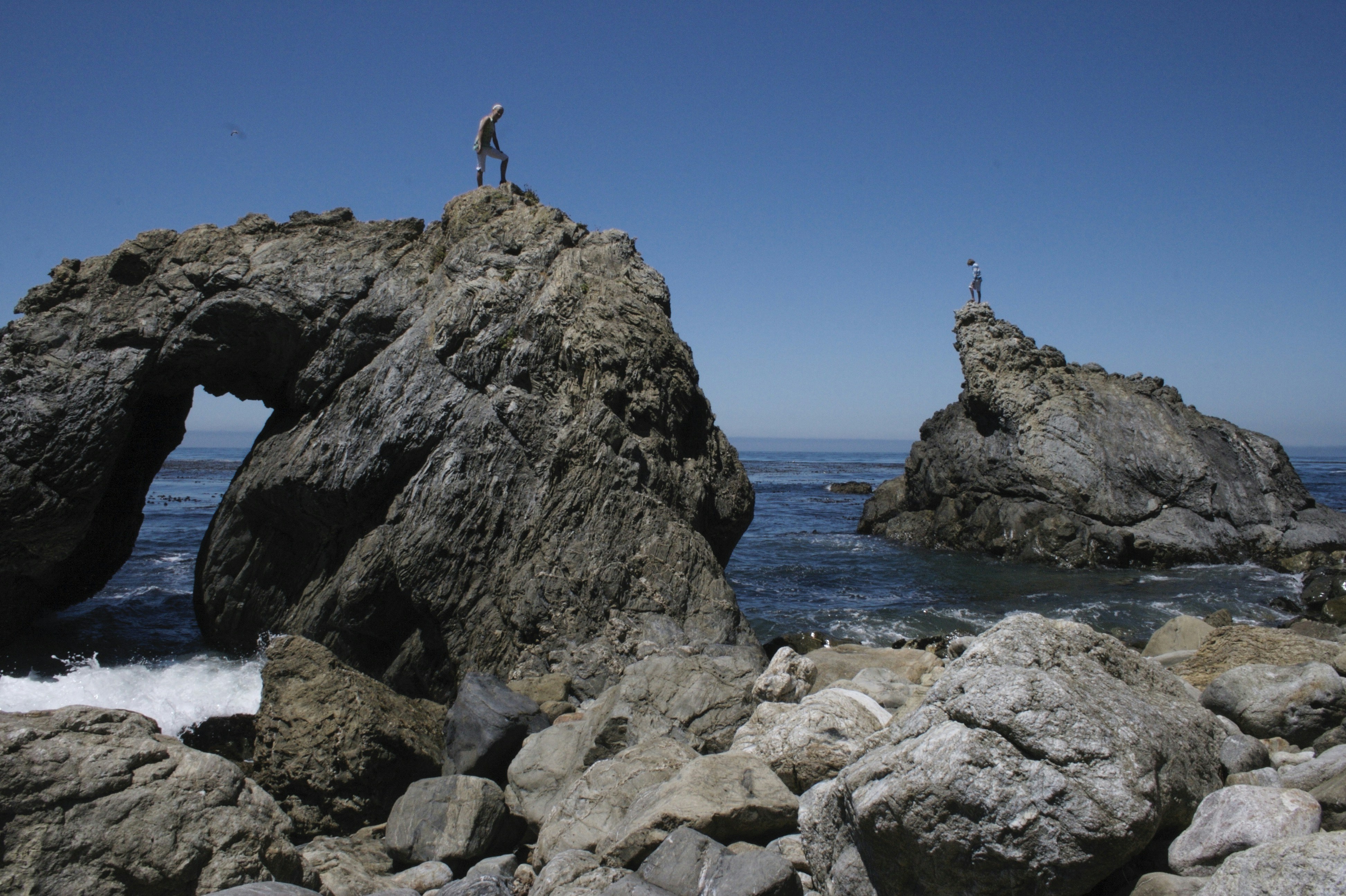  Lone climber silhouette on a jagged coastal arch at midday